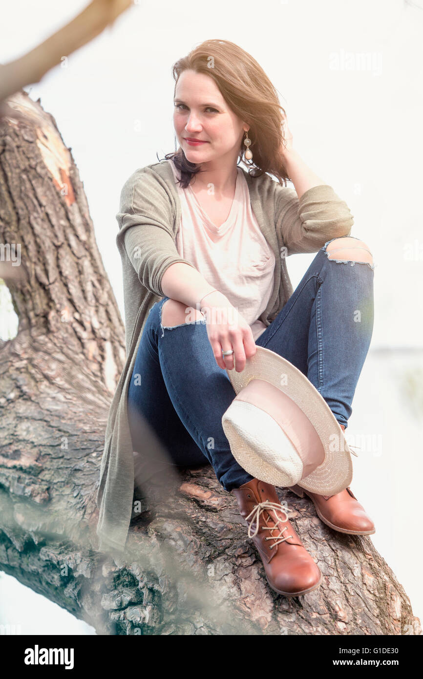 young woman wearing jeans and hat sitting on a tree by the water Stock ...
