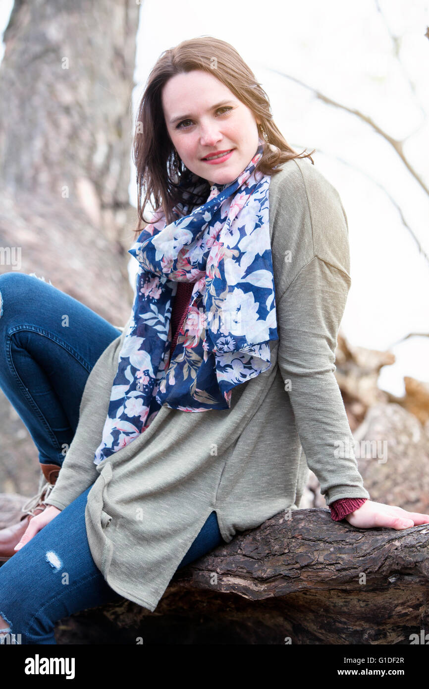 young woman in jeans sitting on a tree by the water Stock Photo - Alamy