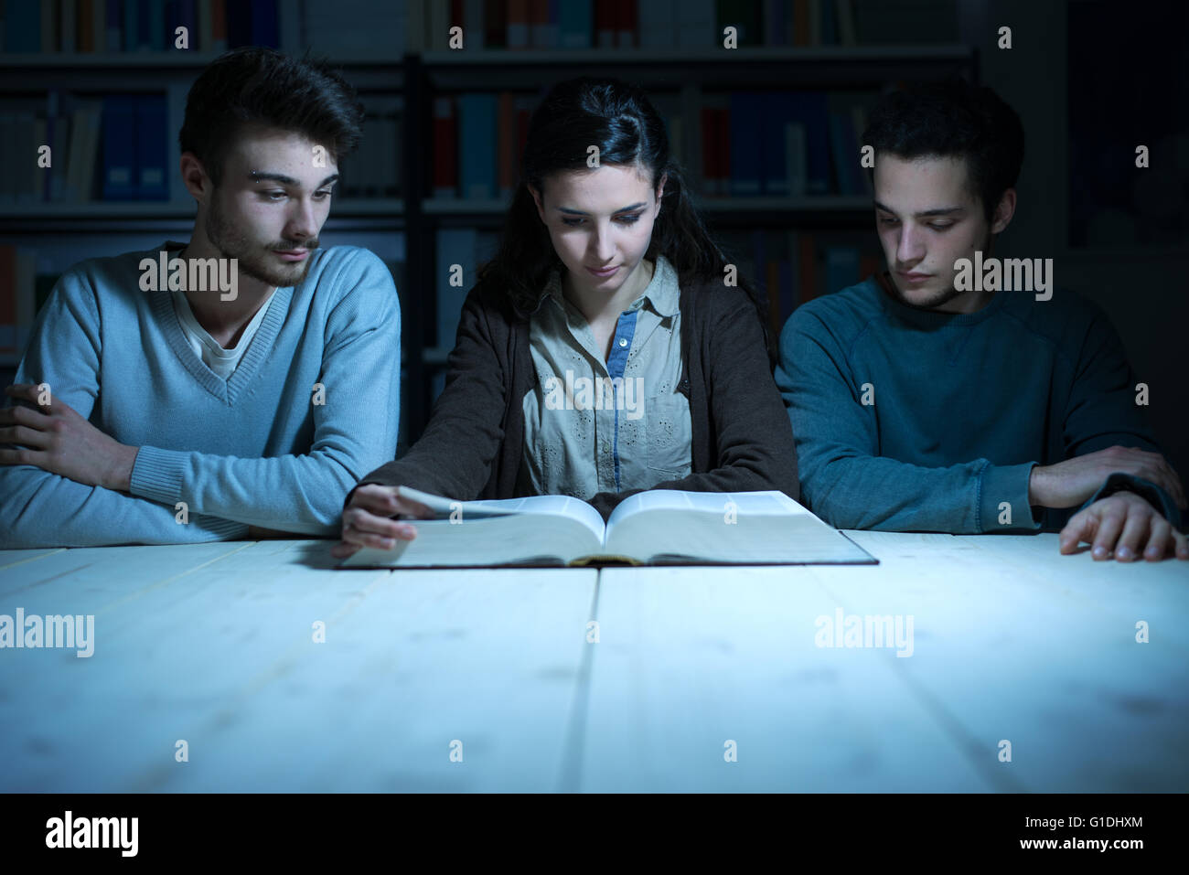 Young college students reading a book together late at night, knowledge ...