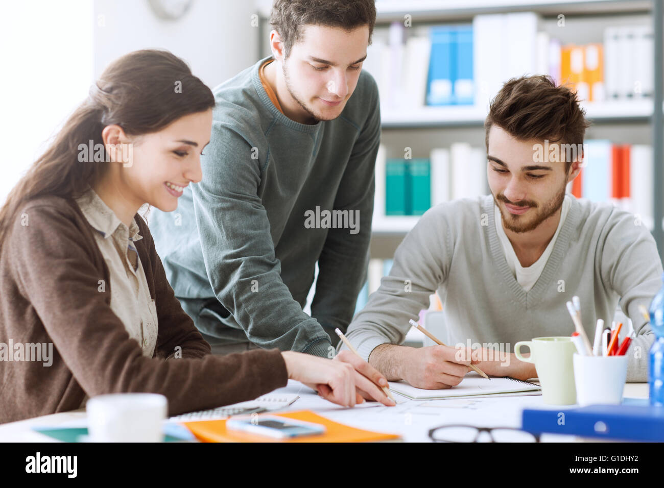 Group of smiling college students studying together at the library and ...