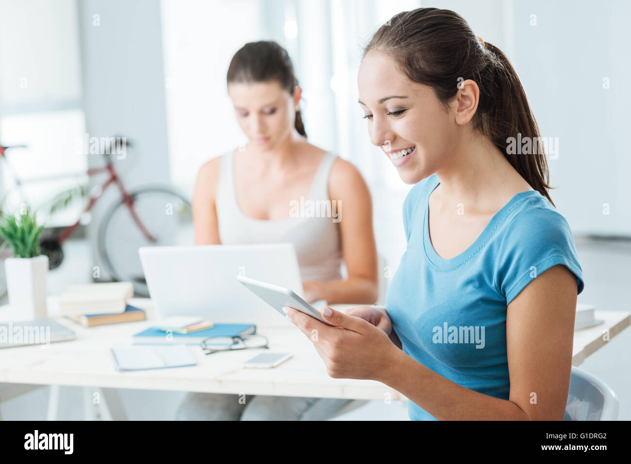 Cute young girl using a digital touch screen tablet, her friend is ...