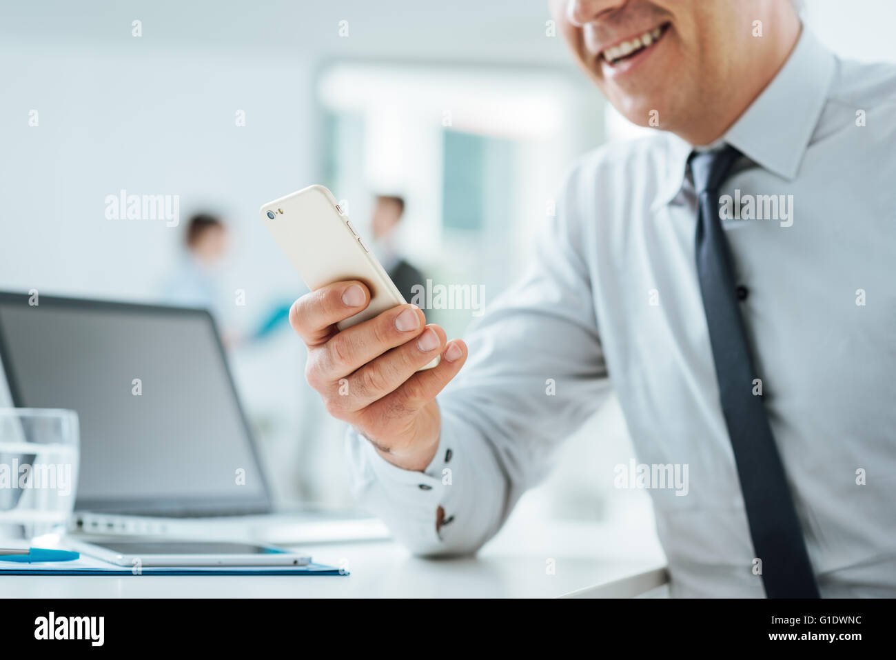 Businessman sitting at office desk using a touch screen smart phone ...