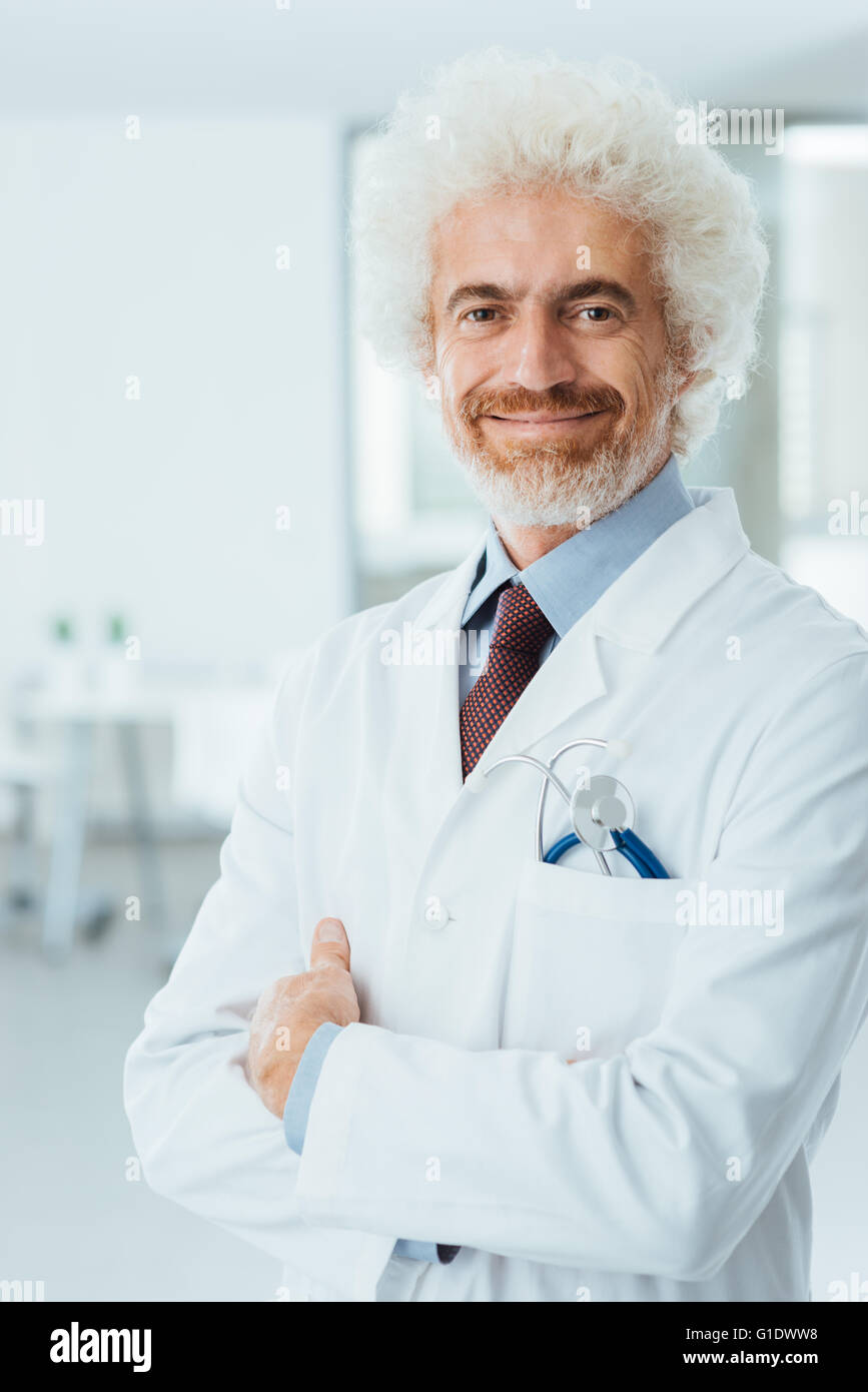Confident doctor at hospital posing with folded arms and smiling at ...