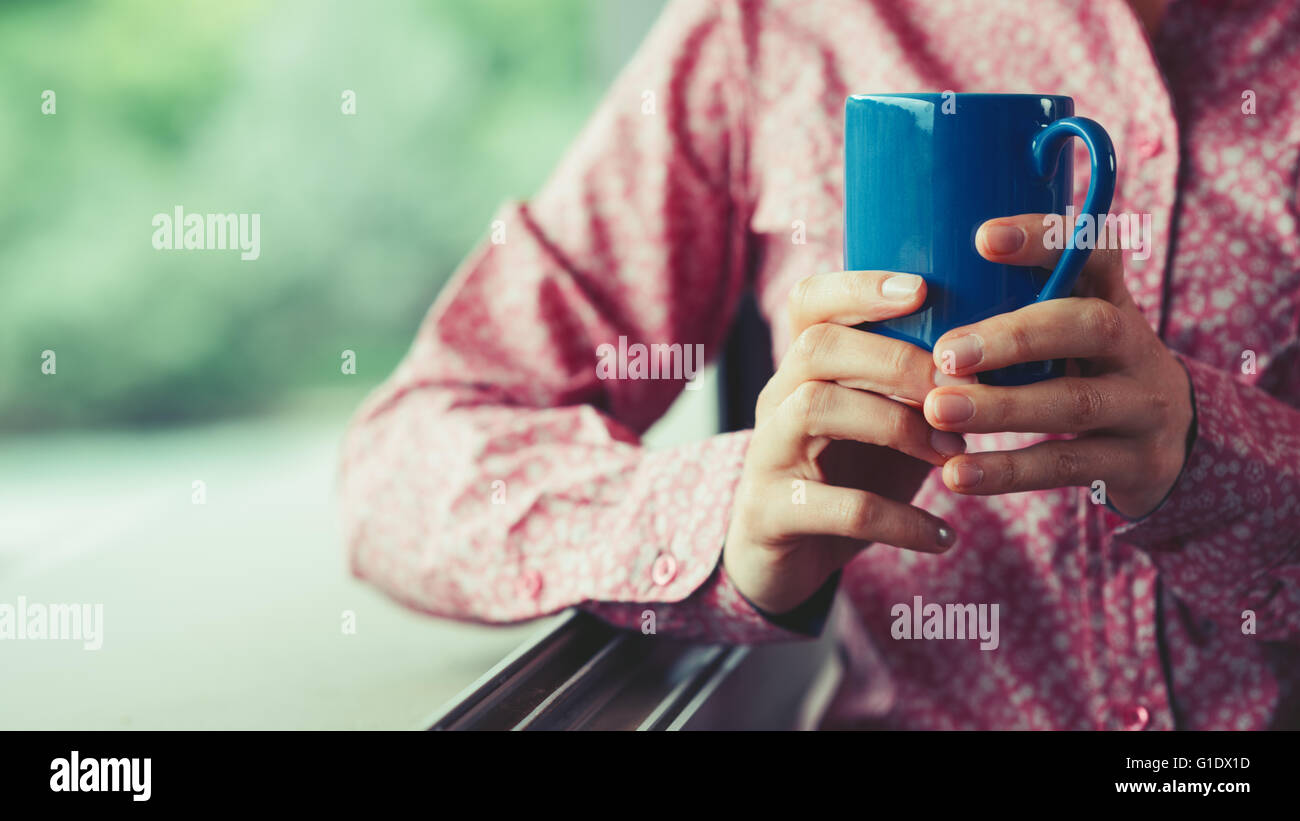 Woman at window holding a cup and having a relaxing coffee break, hands ...