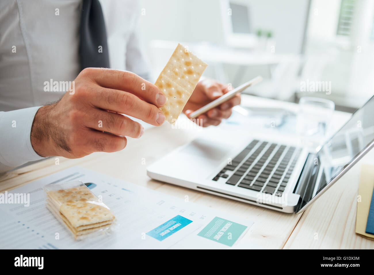 Businessman having a snack at desk holding a cracker and a smart phone ...