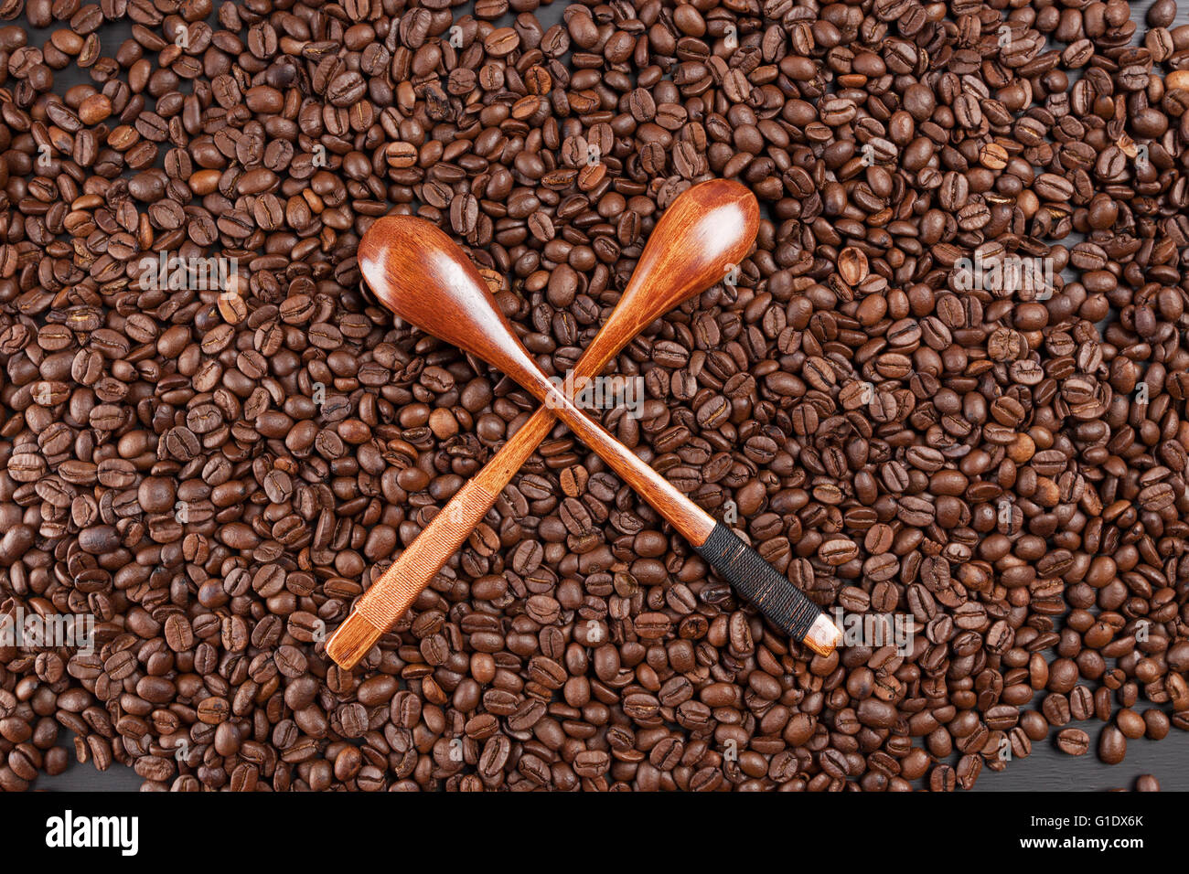 Two crossed wooden spoons placed on scattered roasted coffee beans. Top ...