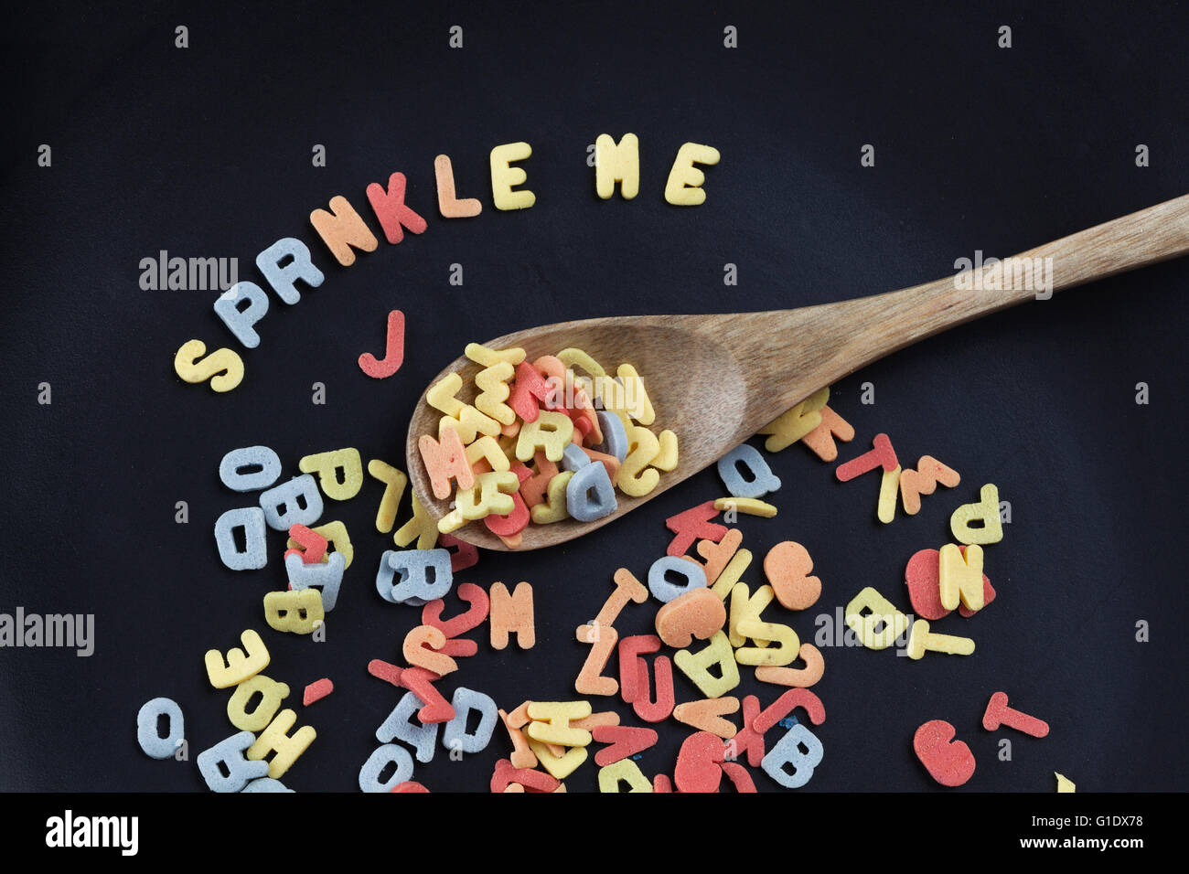 Colorful sprinkles in letter forms with wooden spoon on black plate ...