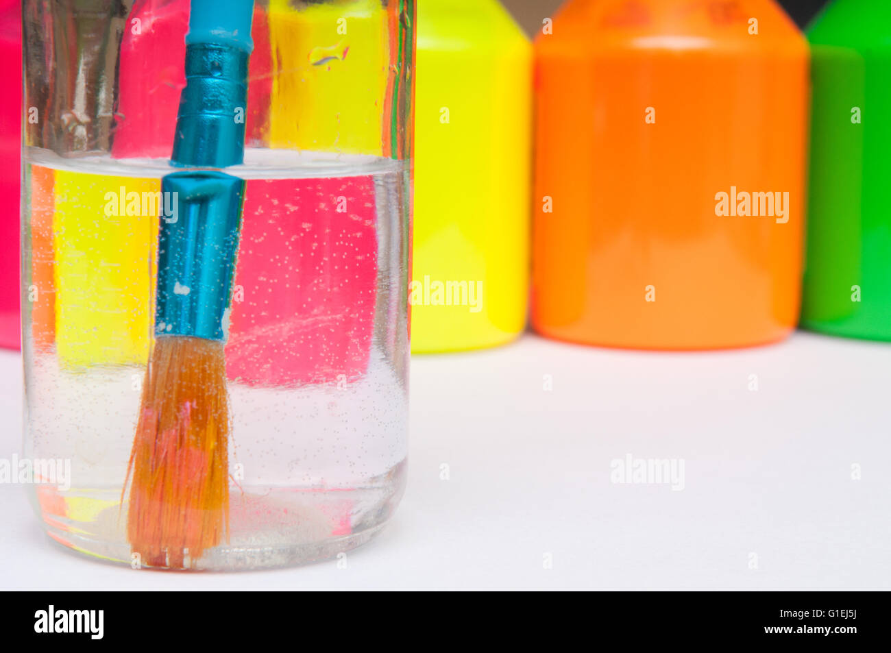 Paint brush in water in front of brightly coloured children's paint ...