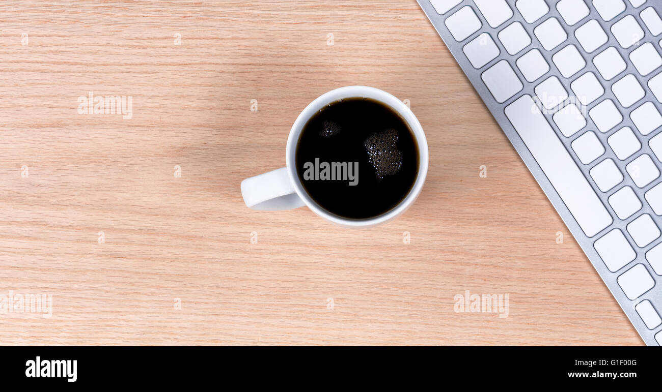 Overhead view of computer keyboard and dark coffee on red oak desktop ...