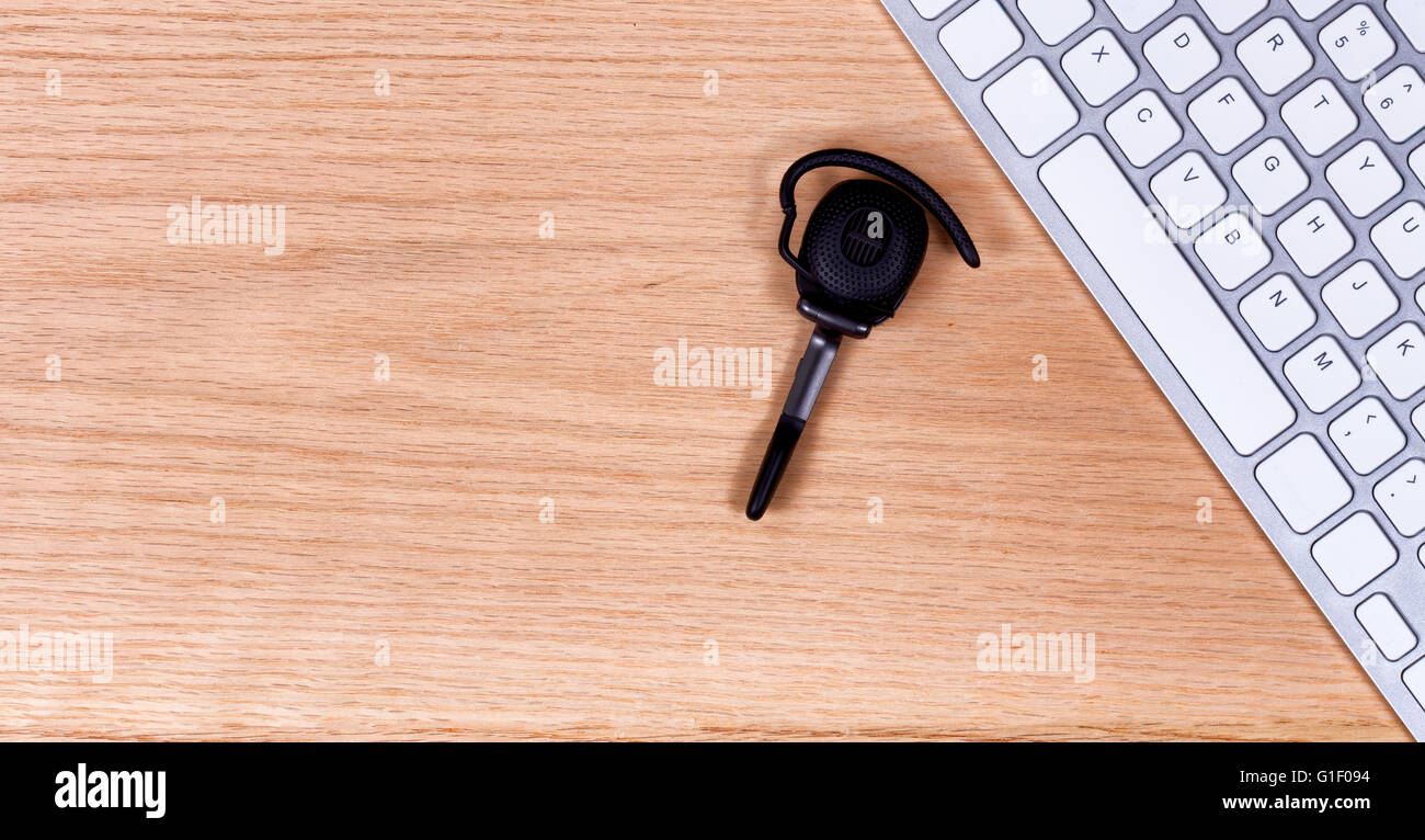 Top view of wireless ear phone piece with computer keyboard on red oak ...