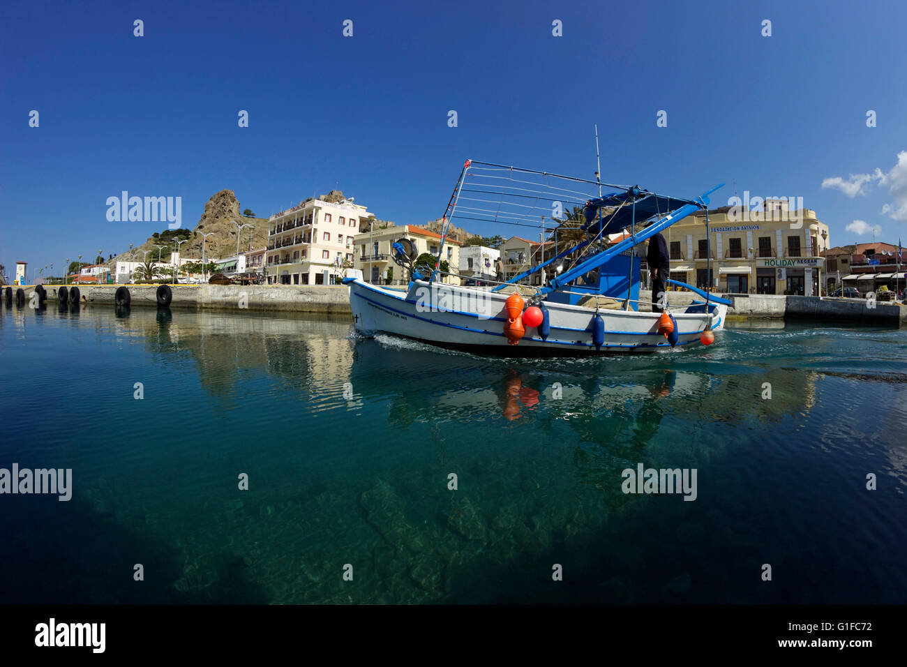 Myrina's promenade mirrored on the limpid sea surface and a fisherman ...