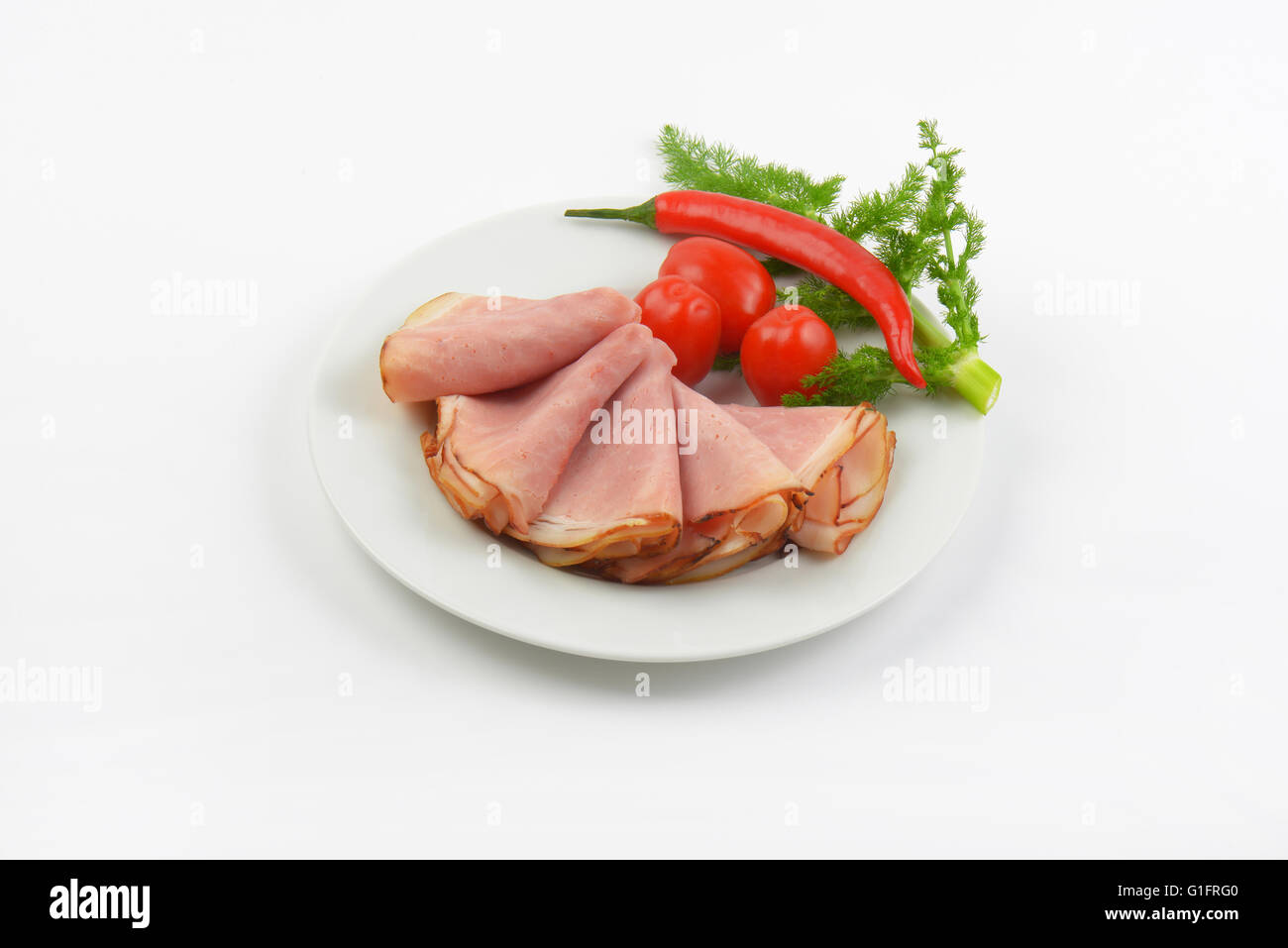 plate of ham slices with vegetable garnish on white background Stock ...