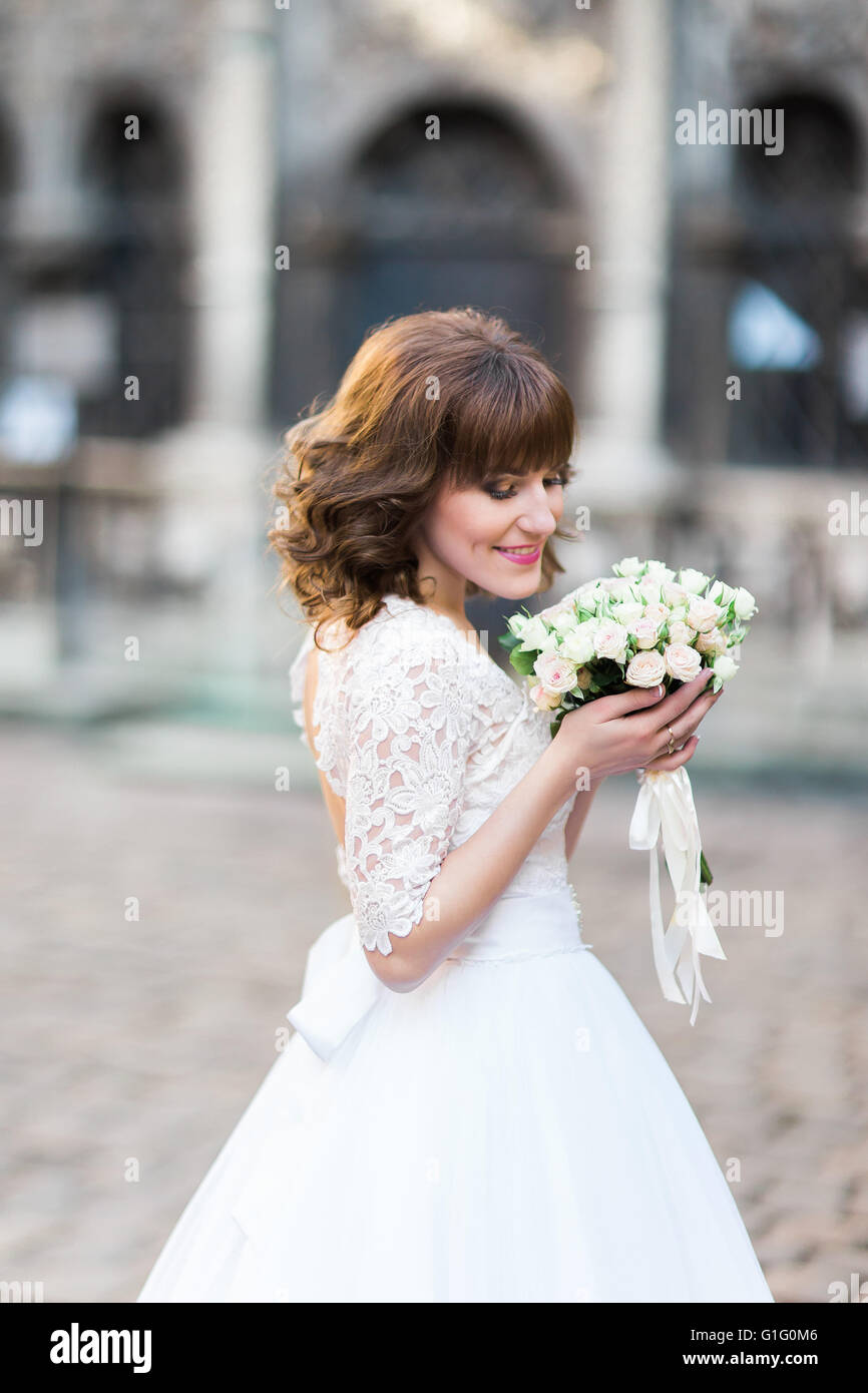 Young smiling bride looking at rose bouquet with cityscape on the ...