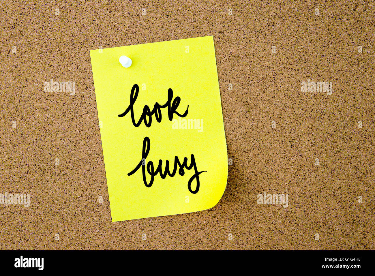 Look Busy written on yellow paper note pinned on cork board with white ...