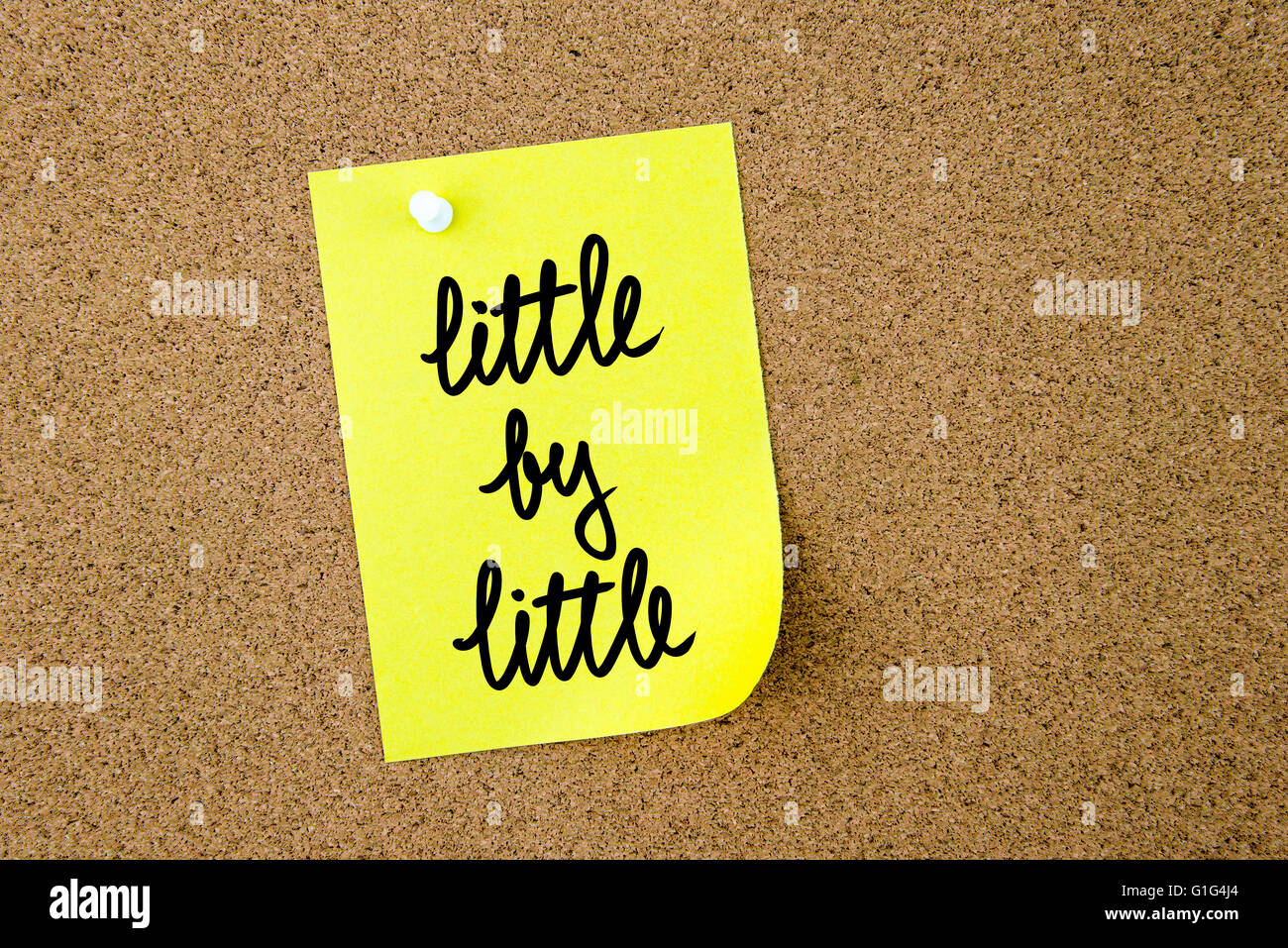 Little By Little written on yellow paper note pinned on cork board with ...
