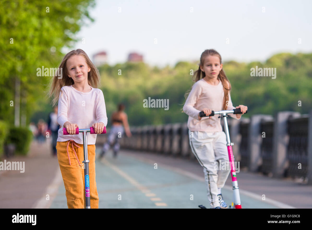 Little adorable girls riding on scooters in park outdoors Stock Photo ...