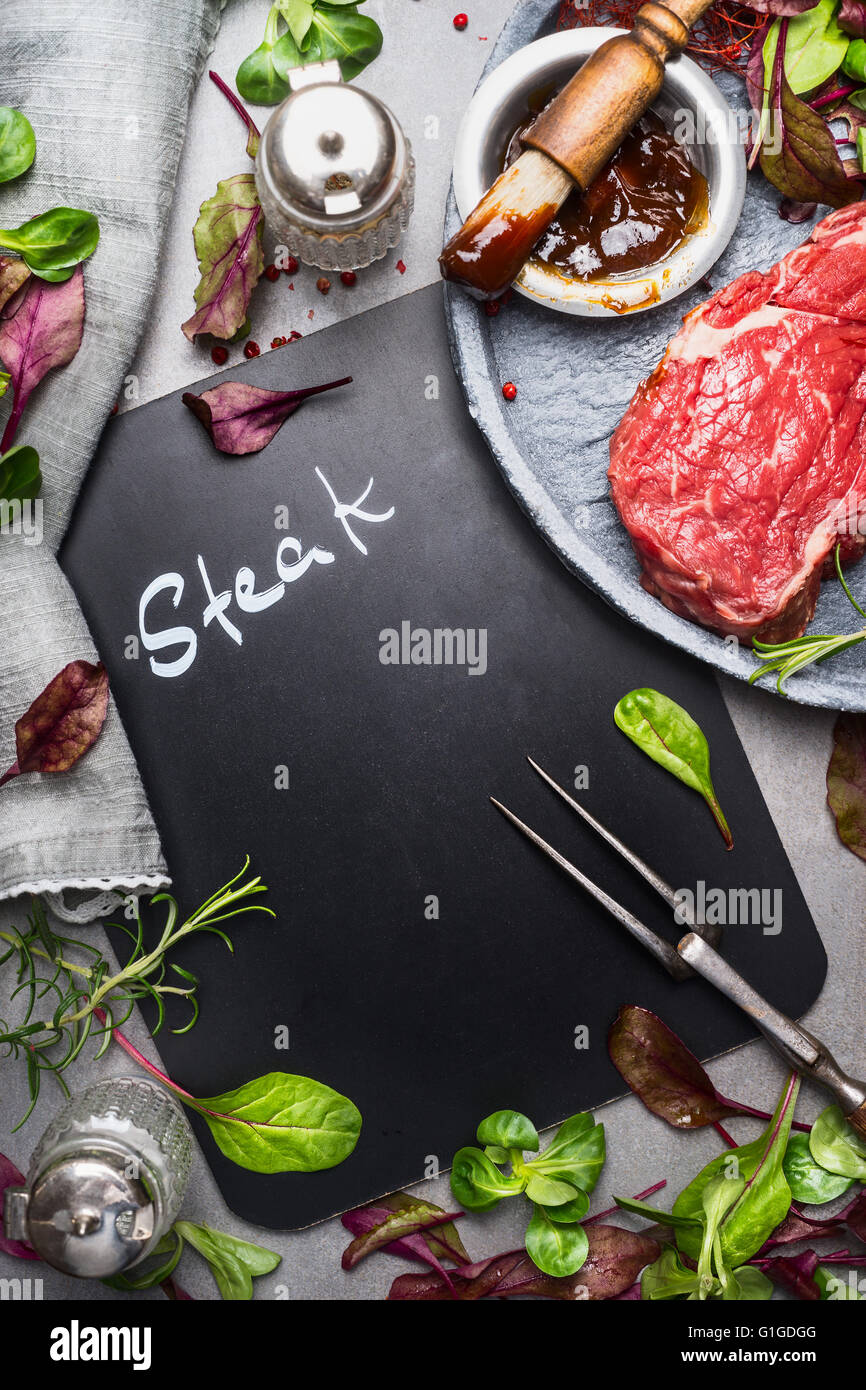 Chalkboard cooking background with raw steak, meat fork,fresh seasoning ...
