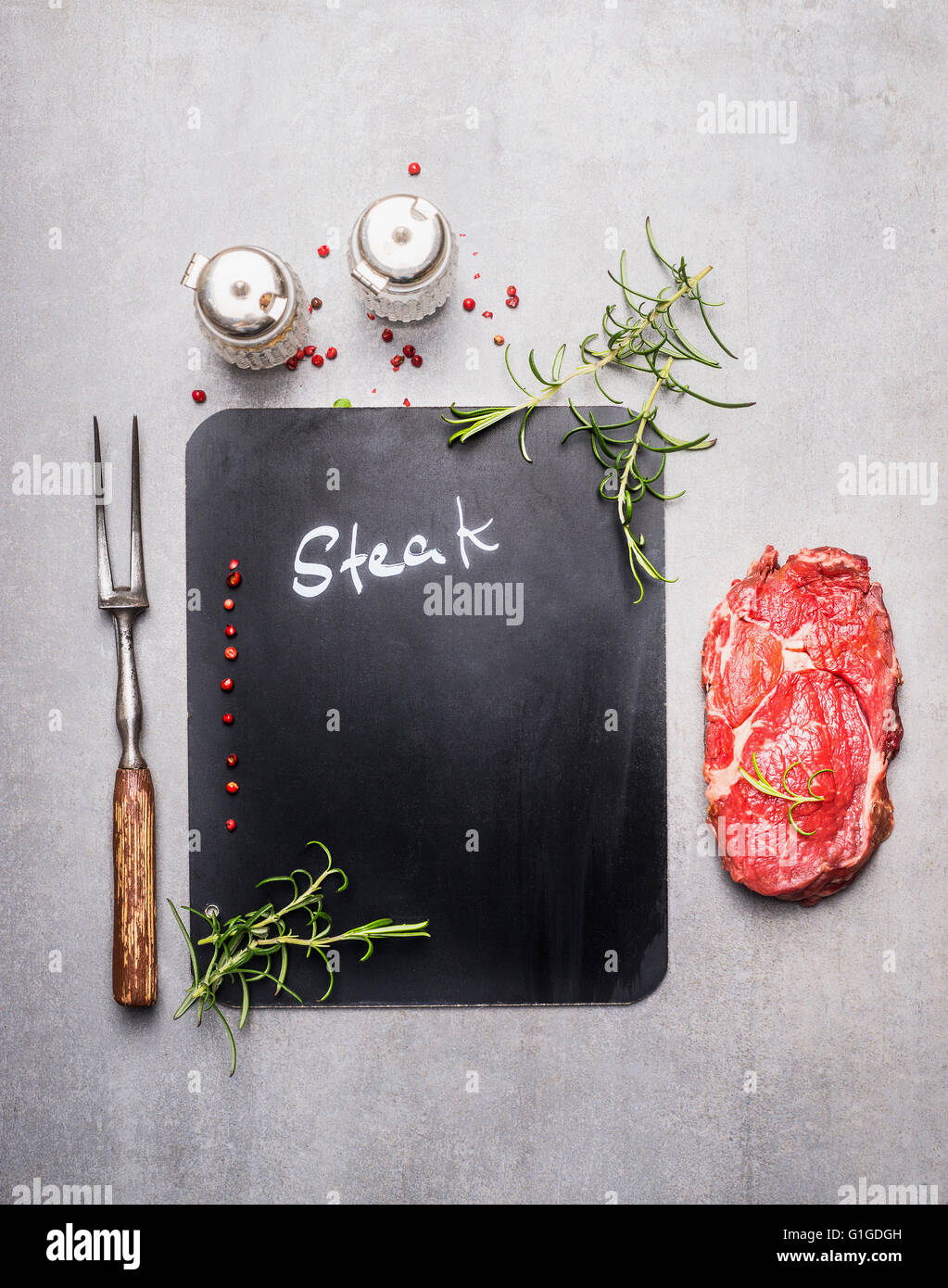 Chalkboard cooking background with raw steak, meat fork, herbs and ...