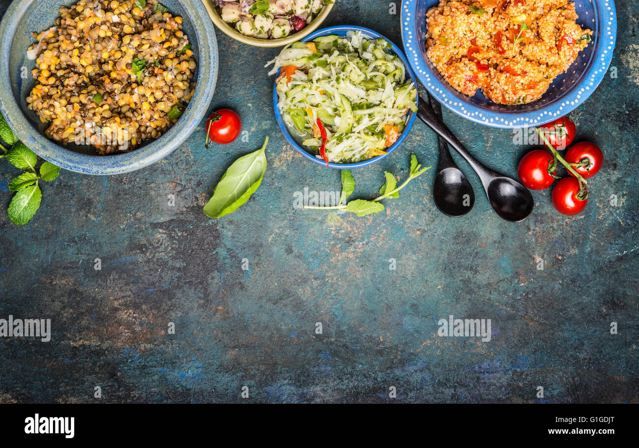 Variety of healthy vegetarian salads in rustic bowls with spoons on ...