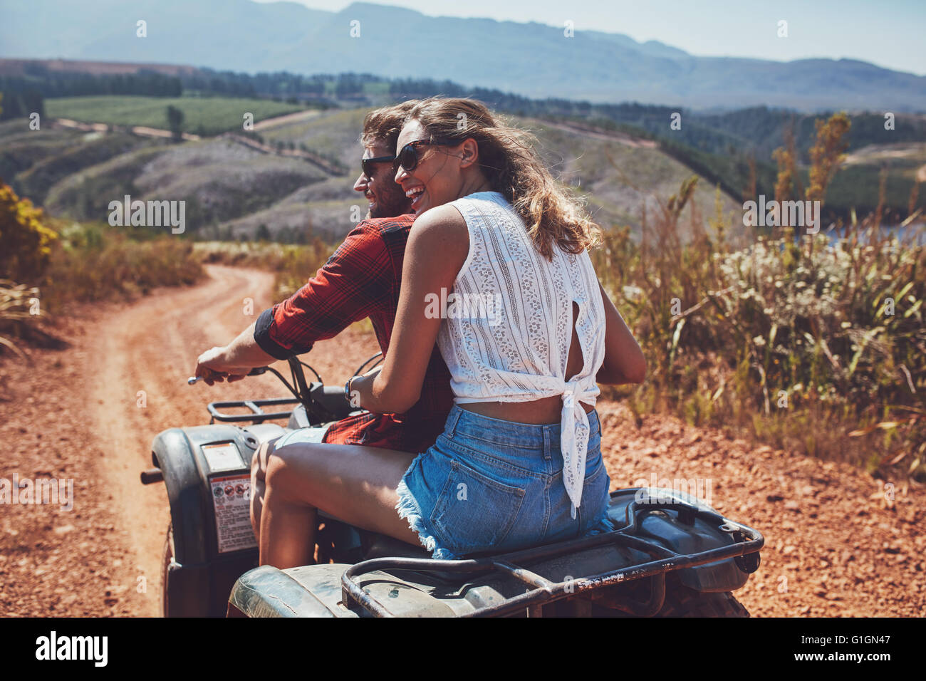 Rear view shot of young couple riding on a quad bike in countryside and ...