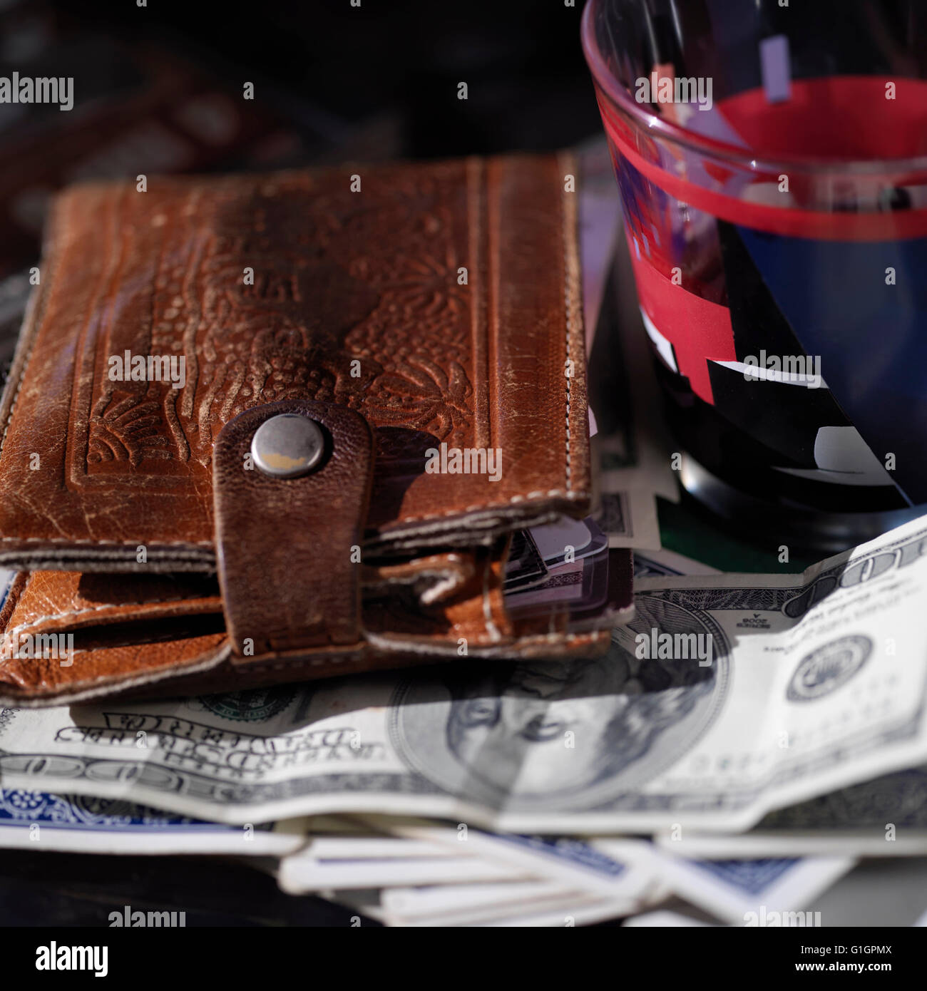 Leather wallet laid on a pile of playing cards and US dollars banknote ...