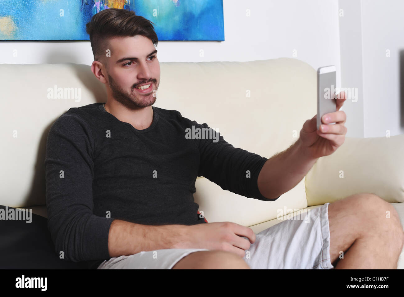 Attractive young man taking selfie with smartphone on white sofa. Indoor Stock Photo - Alamy