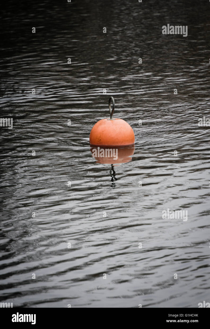 Bright orange nautical buoy floating on slightly rippled water surface ...