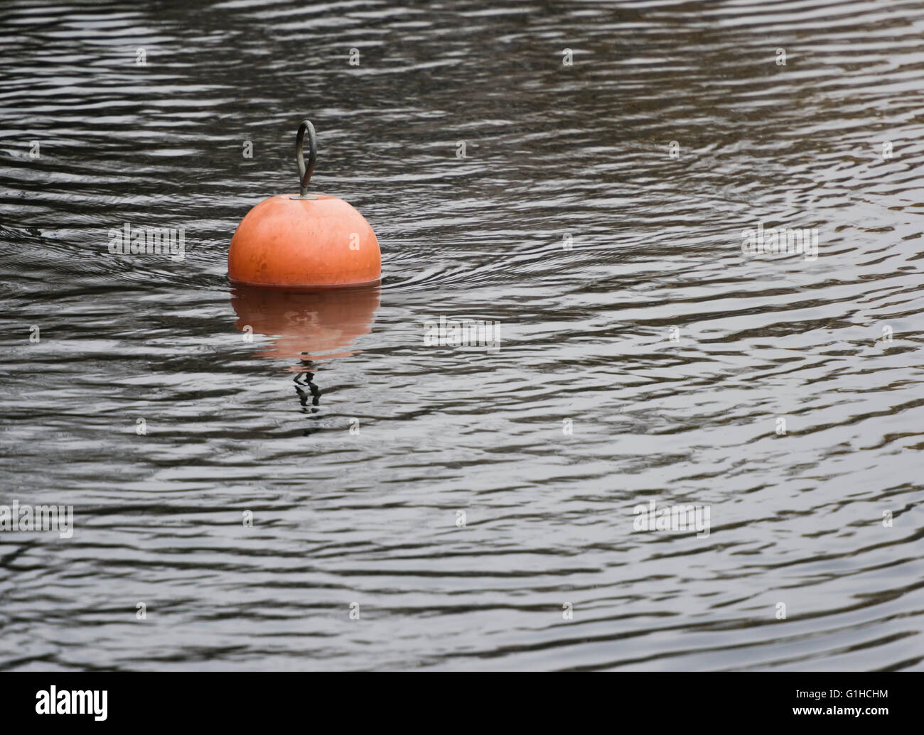 Bright orange nautical buoy floating on slightly rippled water surface ...
