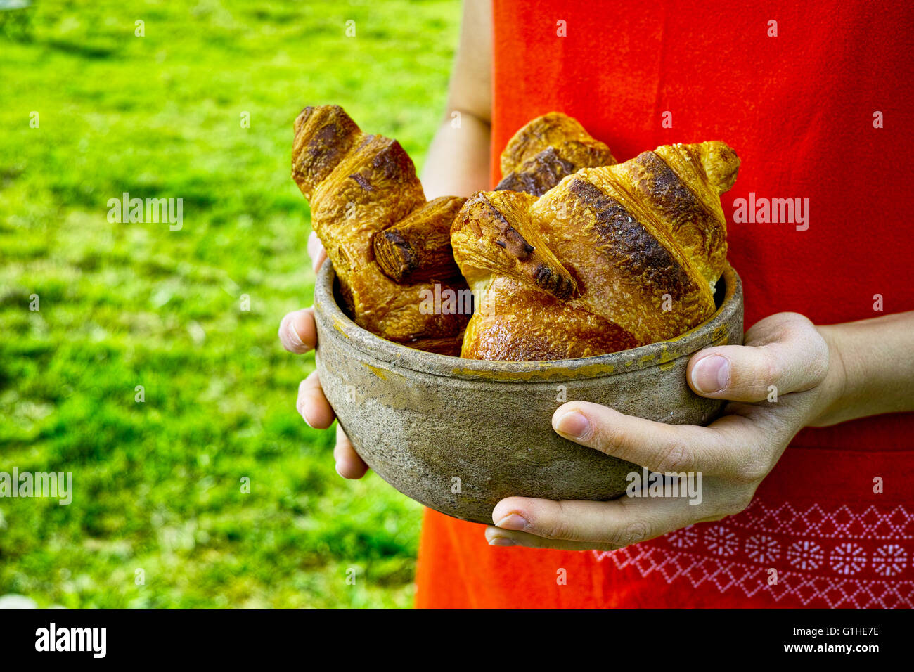 Young woman in red apron holding a plate of fresh baked croissants ...