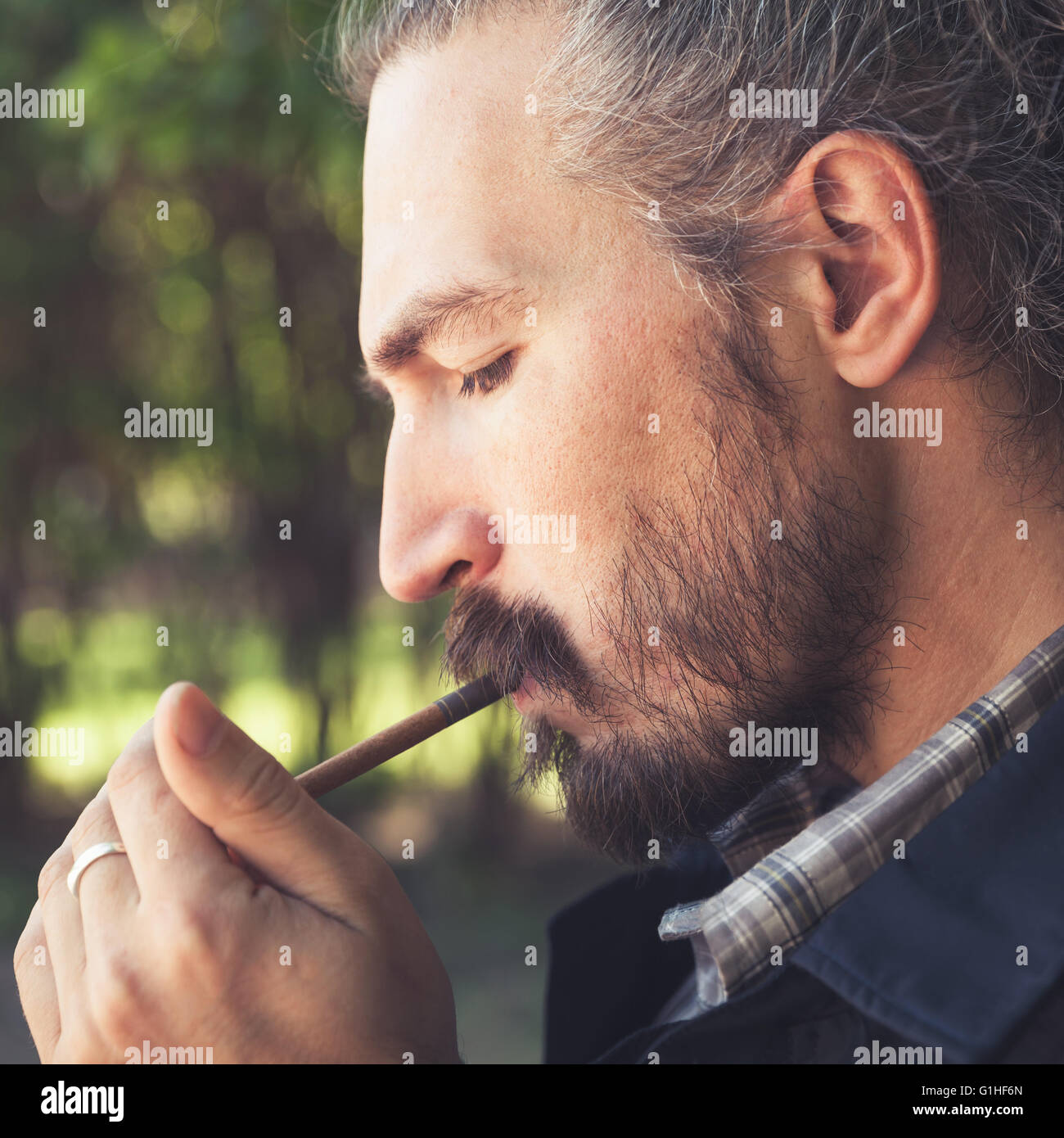 Bearded Asian man lights a cigar, outdoor square profile portrait with ...