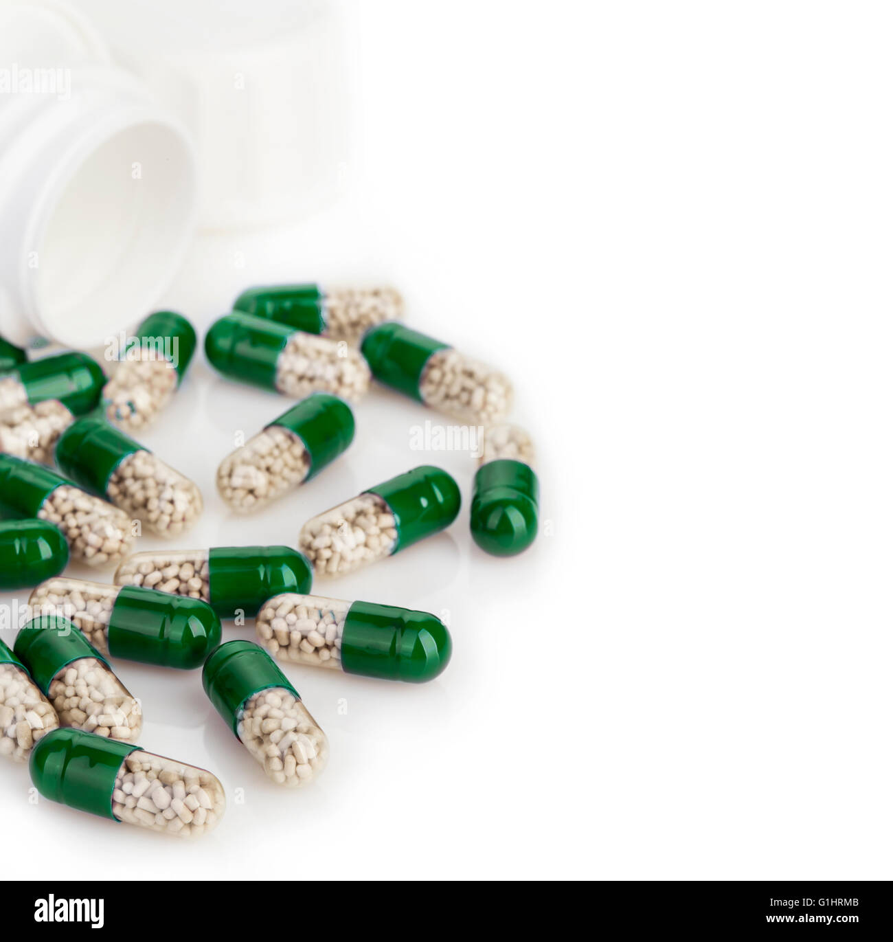 Green capsules, pills poured out of a white bottle close-up on a white ...