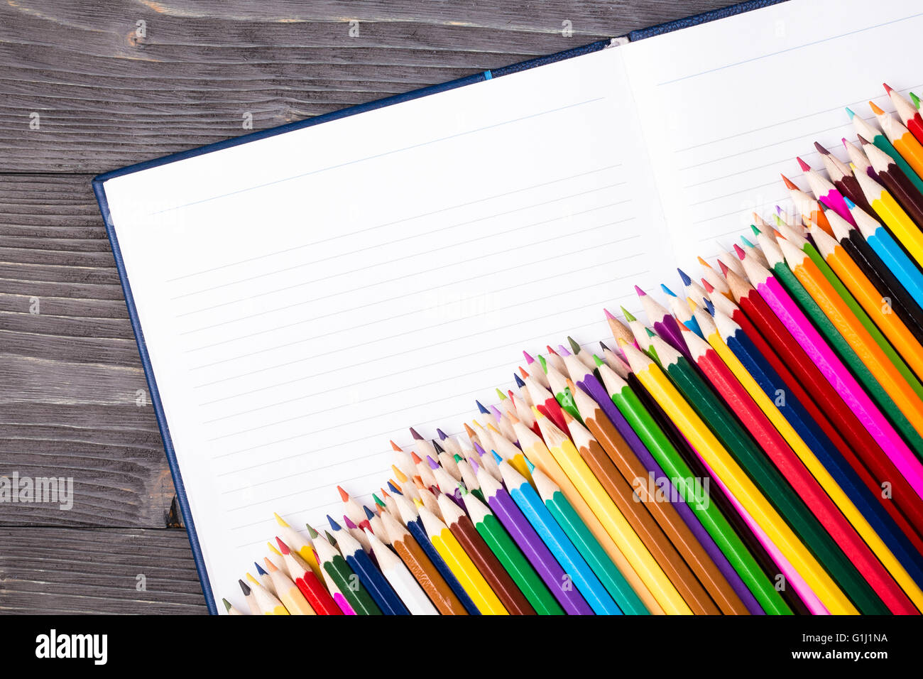 Bunch of color pencils and open notebook on gray wooden background with ...