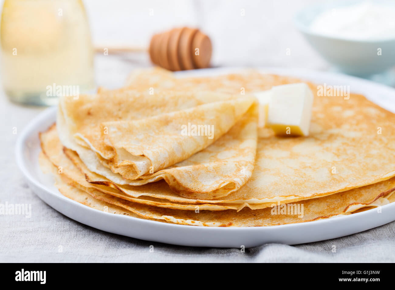 Thin crepes or pancakes with butter, honey and sour cream on a rustic ...