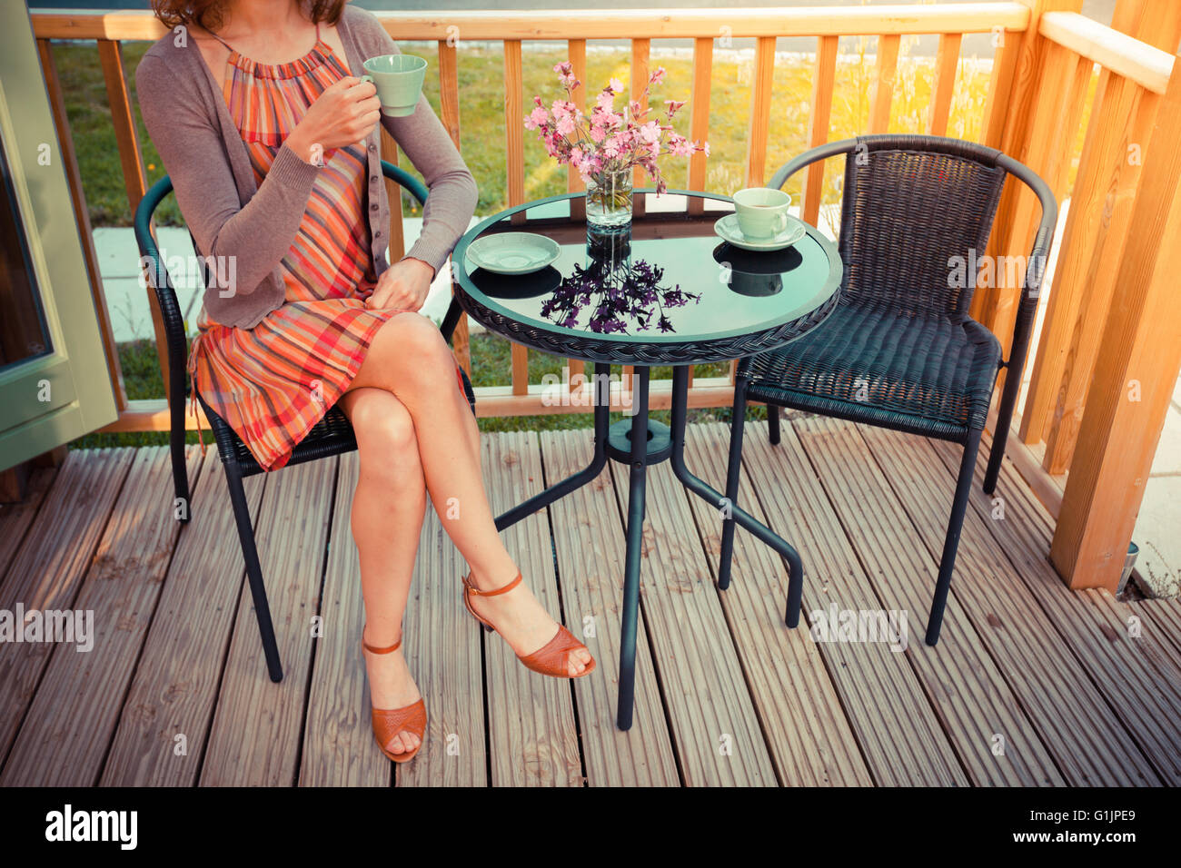 A young woman is sitting and drinking tea on the porch in summer Stock ...