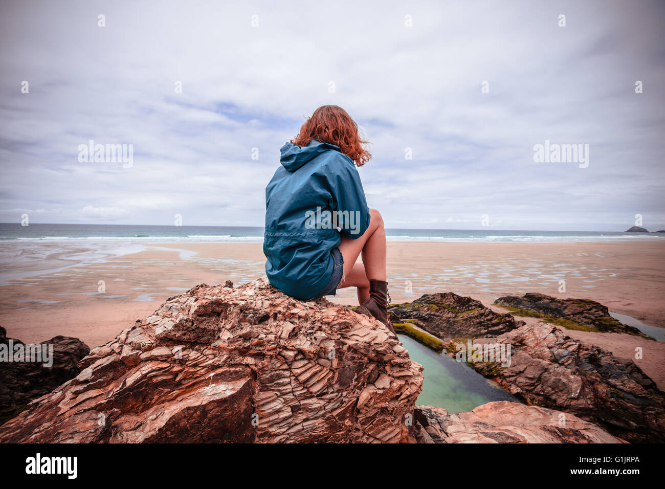 A young woman is sitting on a rock on the beach Stock Photo - Alamy