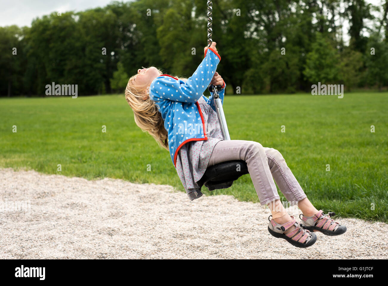 Happy Child blond girl (age 5) rids on Flying Fox play equipment in a ...