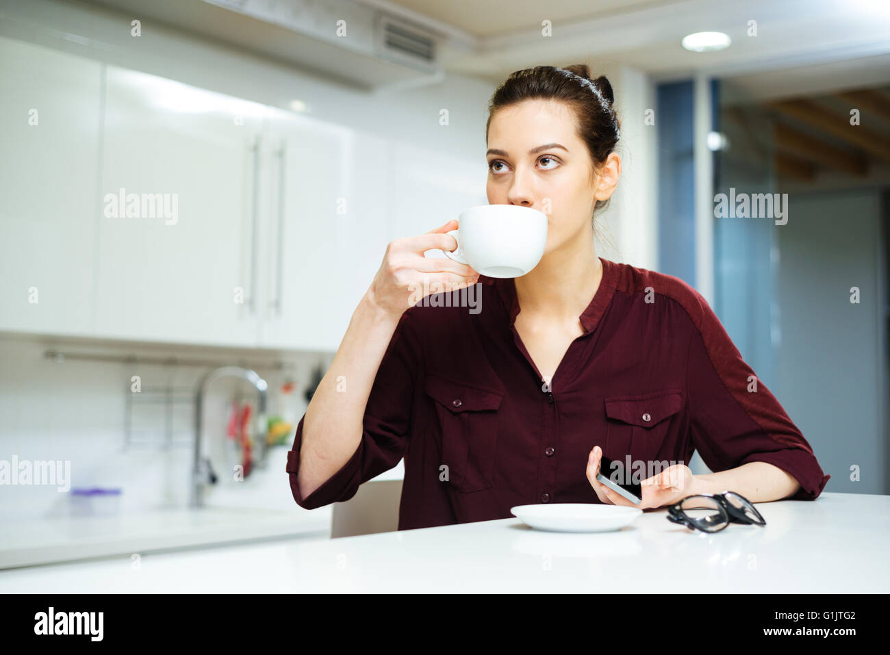 Beautiful young woman sitting and drinking coffee on the kitchen Stock ...