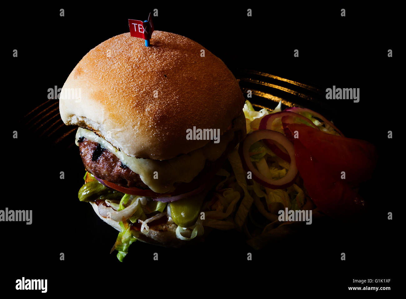 Side-lit large burger with cheese, lettuce, tomato, onion and gherkin ...