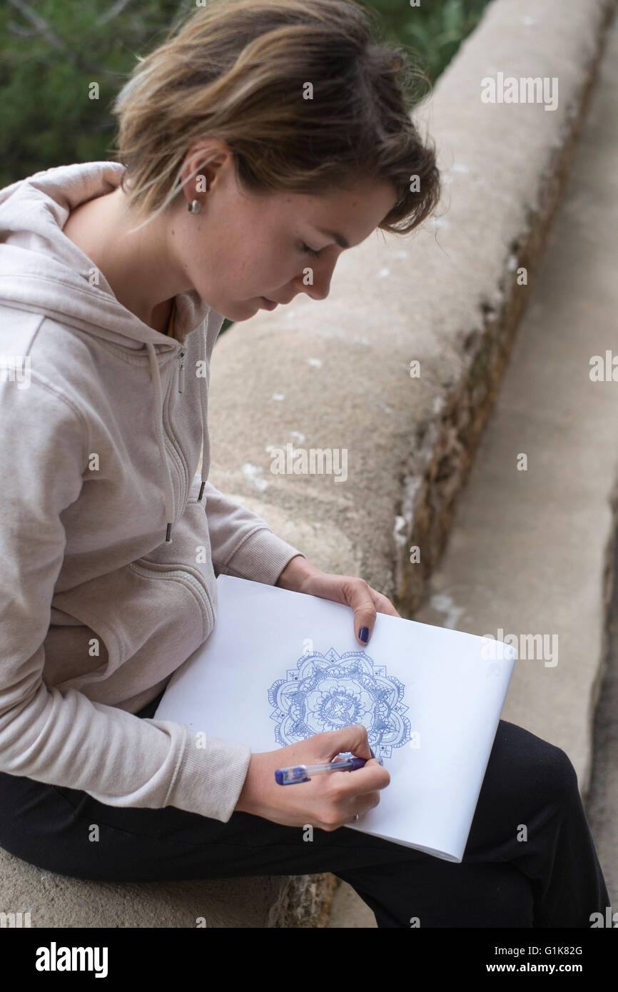 Young woman drawing a mandala pattern on a sketchpad with a violet ...