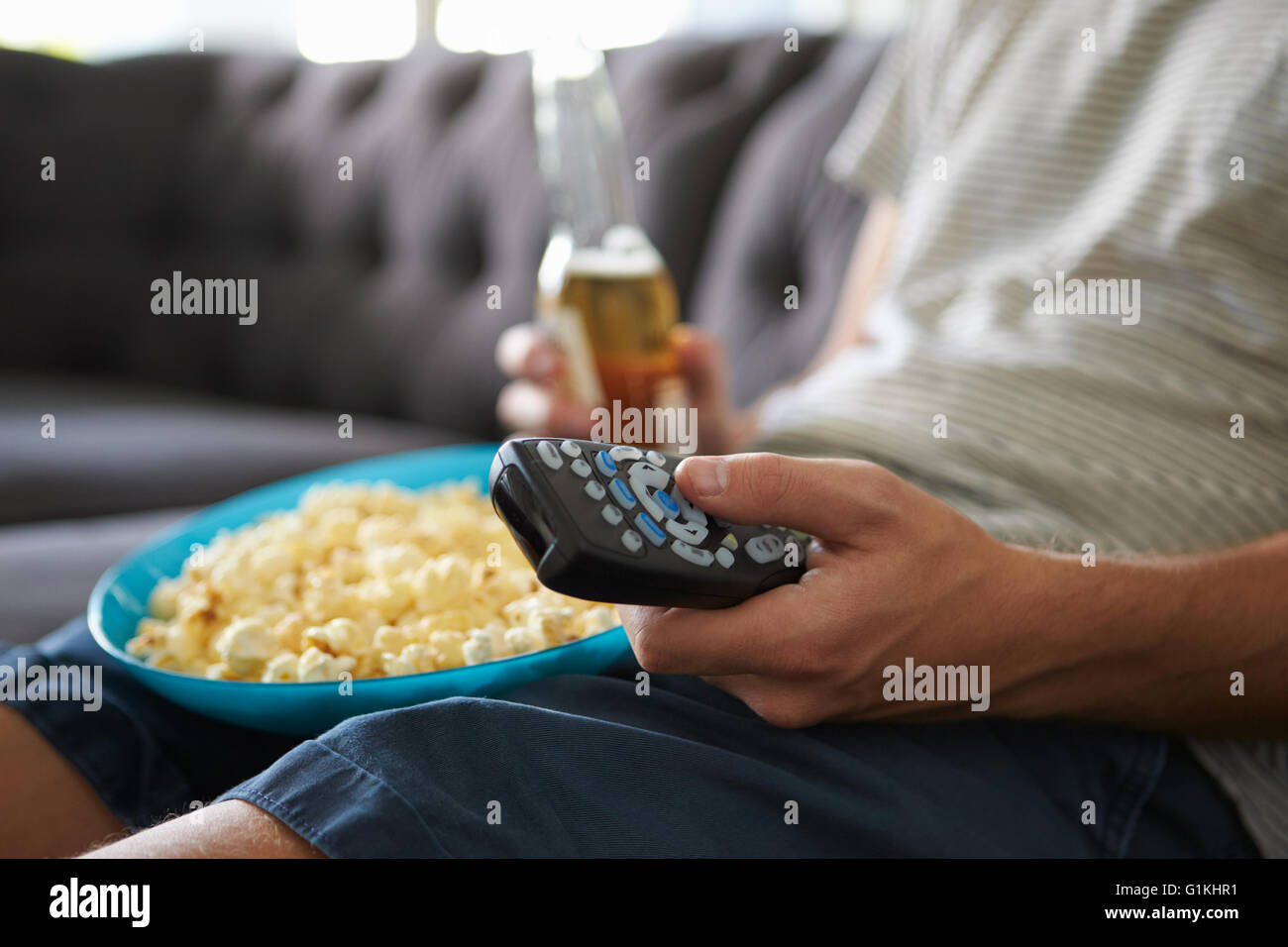Man Sitting On Sofa Holding TV Remote And Bottle Of Beer Stock Photo ...