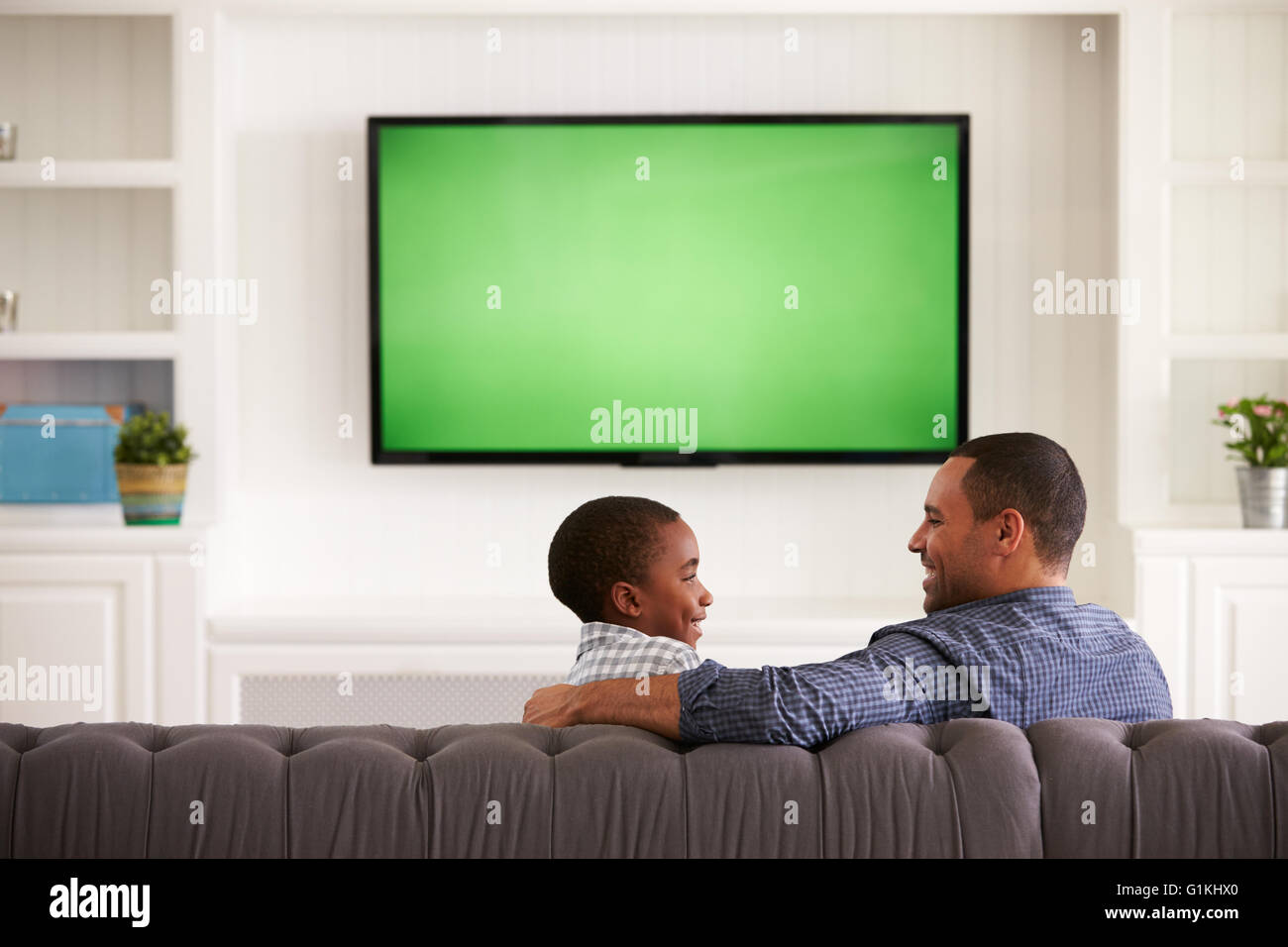 Father and son watching TV looking at each other, back view Stock Photo ...
