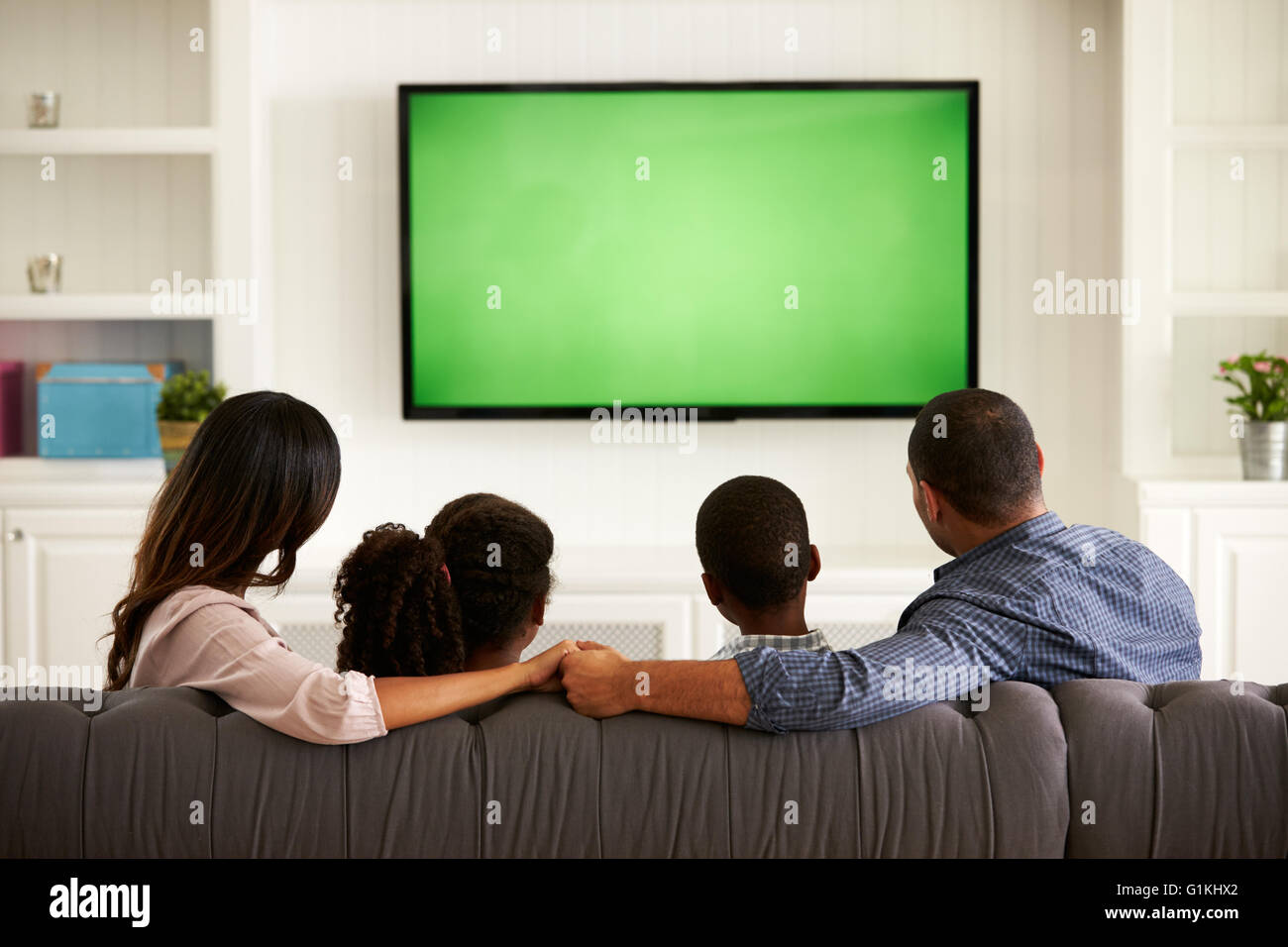 Parents and their two children watching TV together at home Stock Photo ...