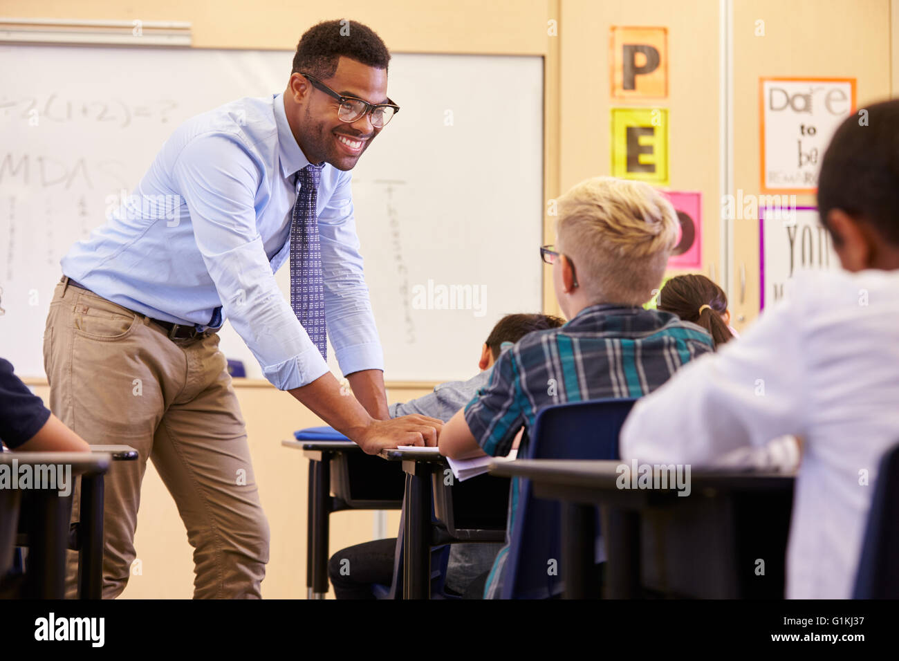 Smiling teacher leaning on elementary school pupil’s desk Stock Photo ...