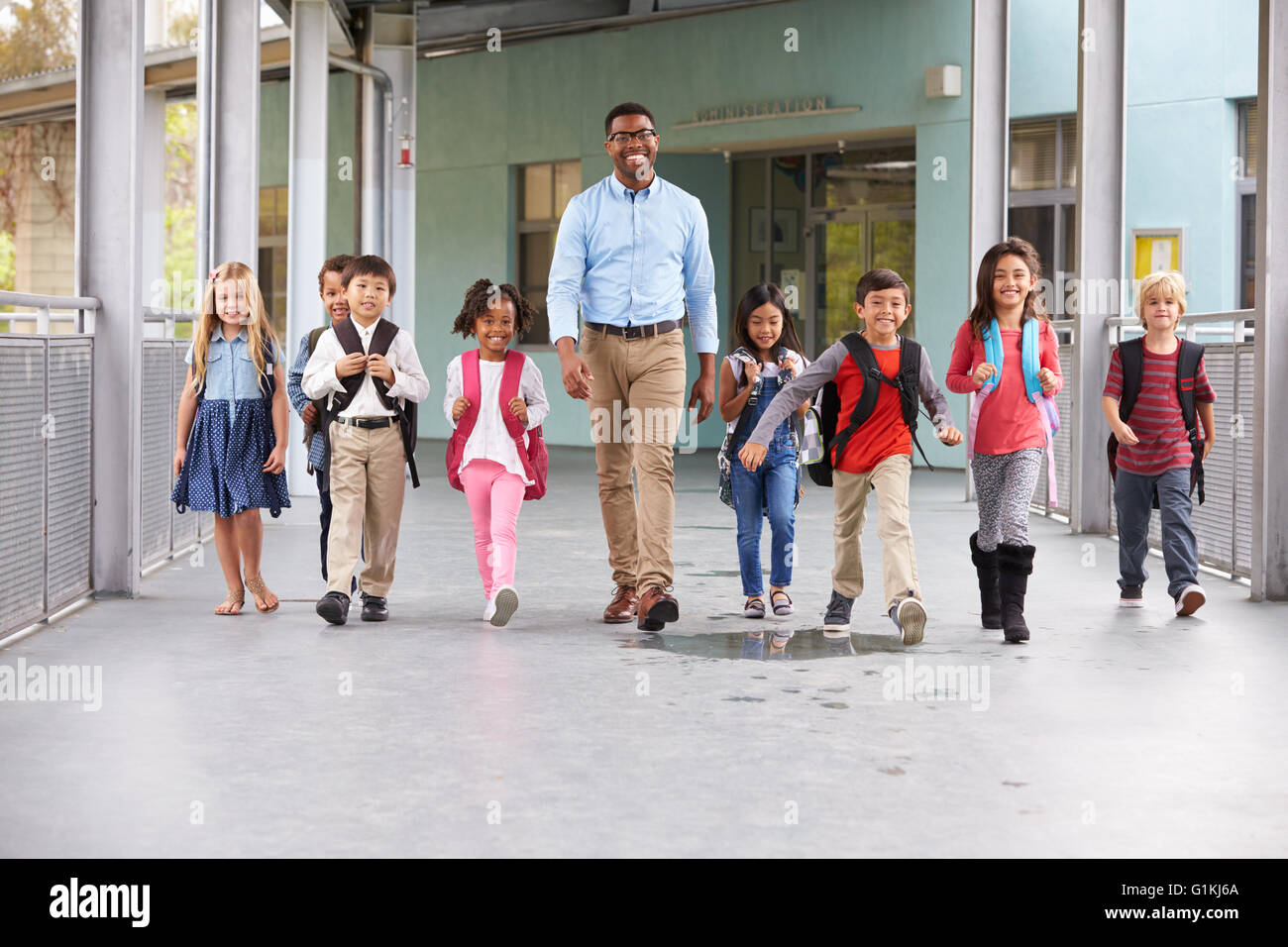 Male teacher walking in corridor with elementary school kids Stock ...