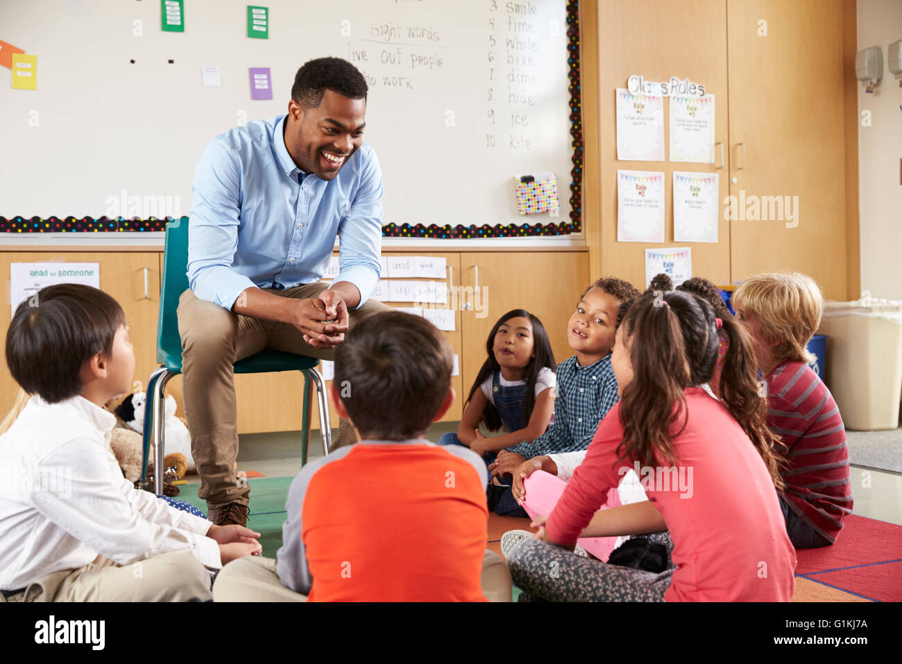 Elementary school kids sitting around teacher in a classroom Stock ... Elementary school kids sitting around teacher in a classroom Stock ...