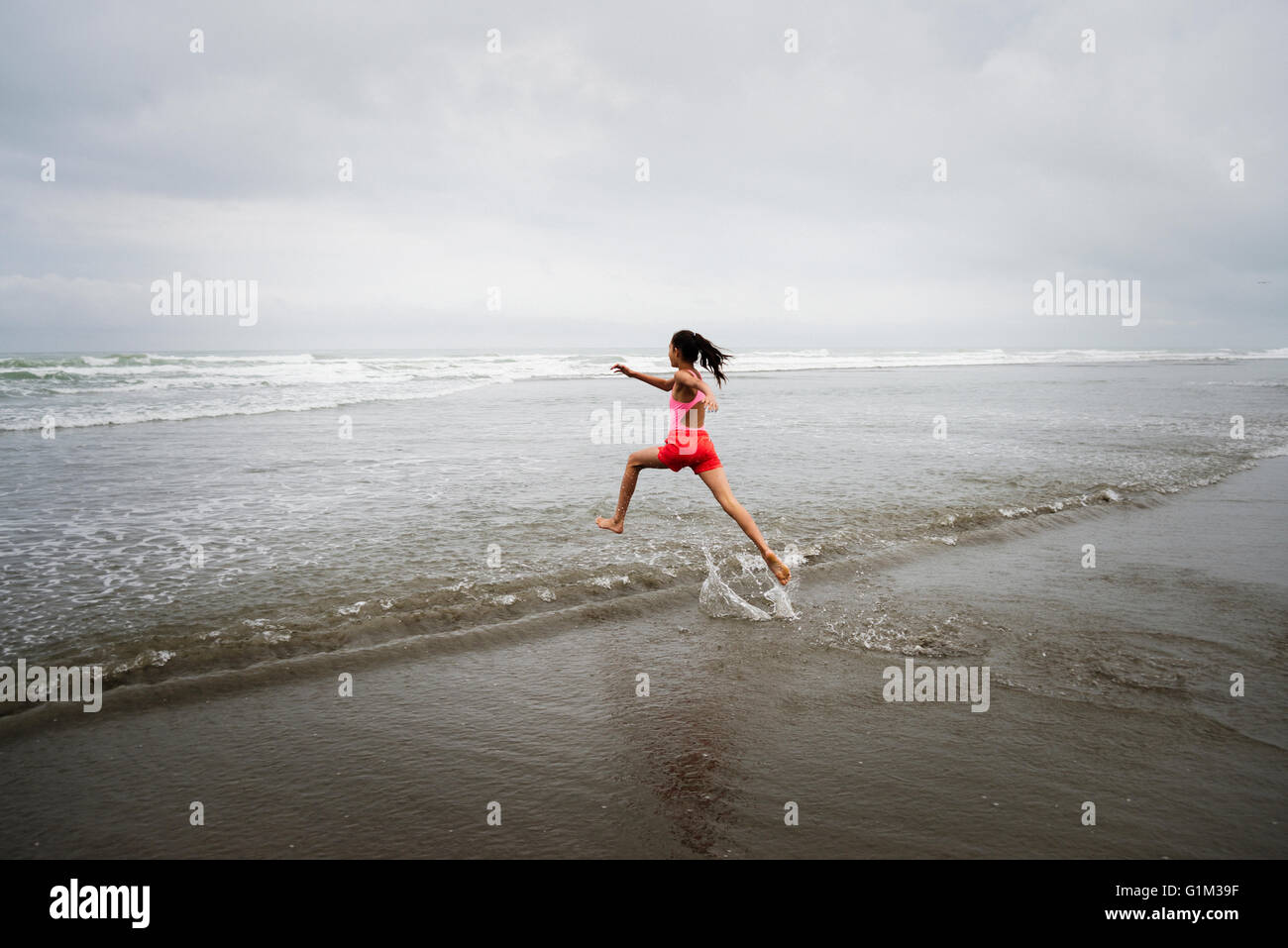 Mixed race girl running into ocean on beach Stock Photo - Alamy