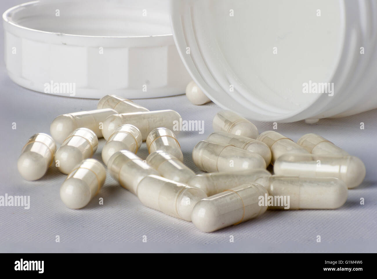 Capsules on white, white container in the back Stock Photo - Alamy