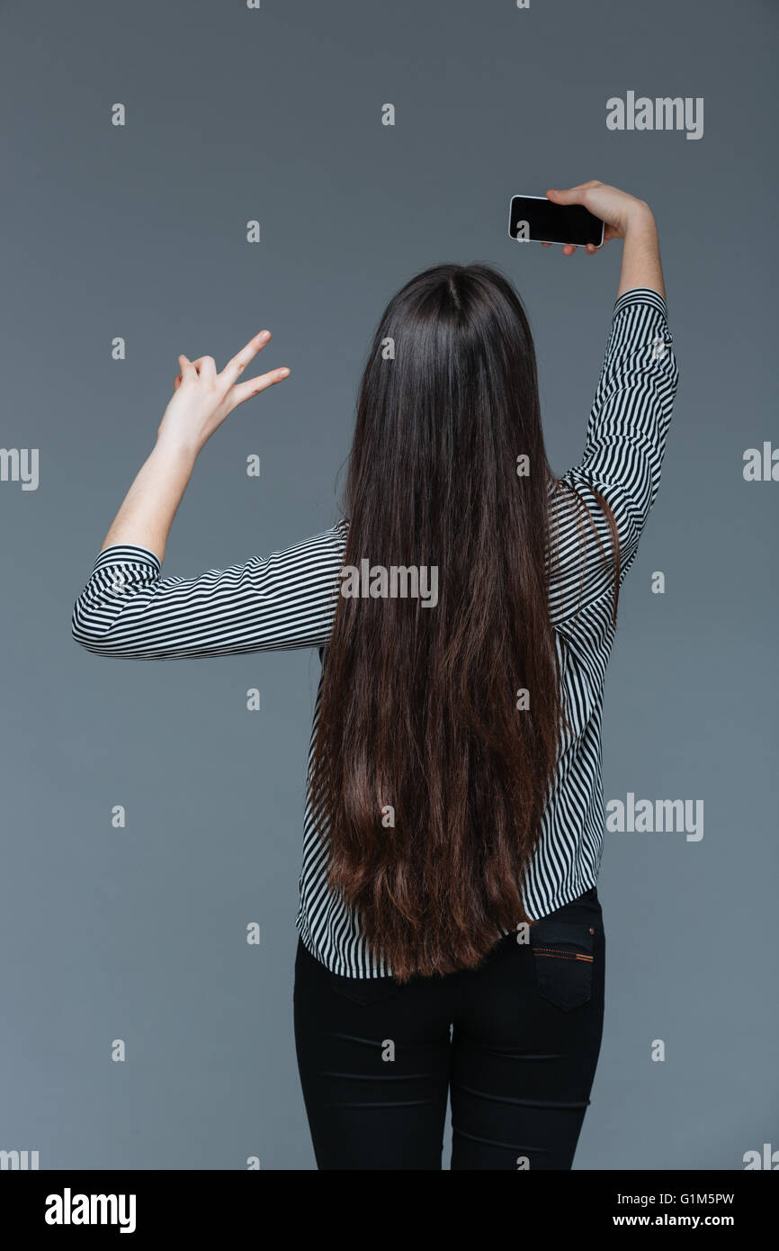 Back view portrait of a young woman making selfie photo on smartphone ...