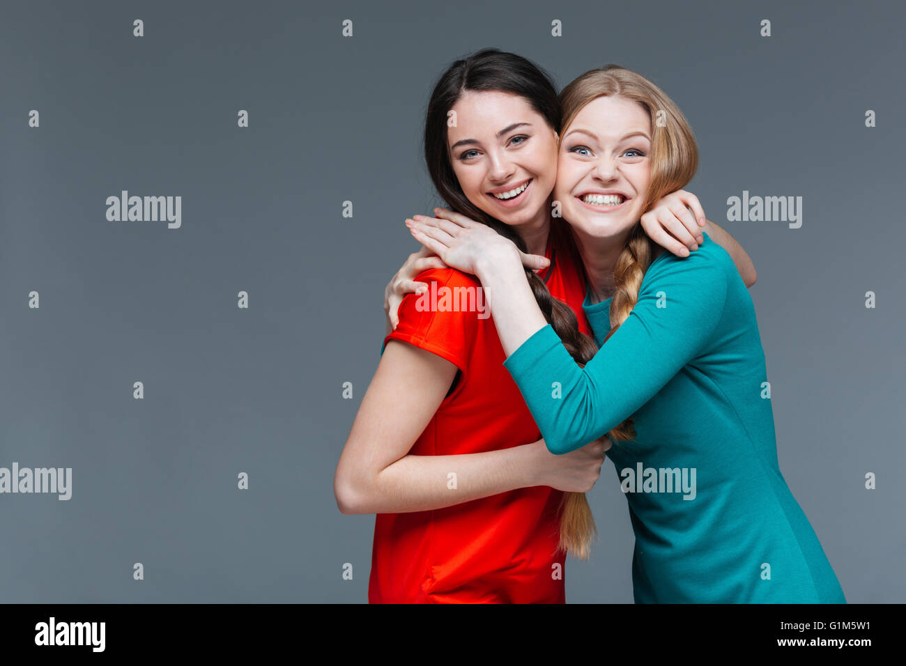 Two cheerful beautiful young women standing and hugging over grey ...