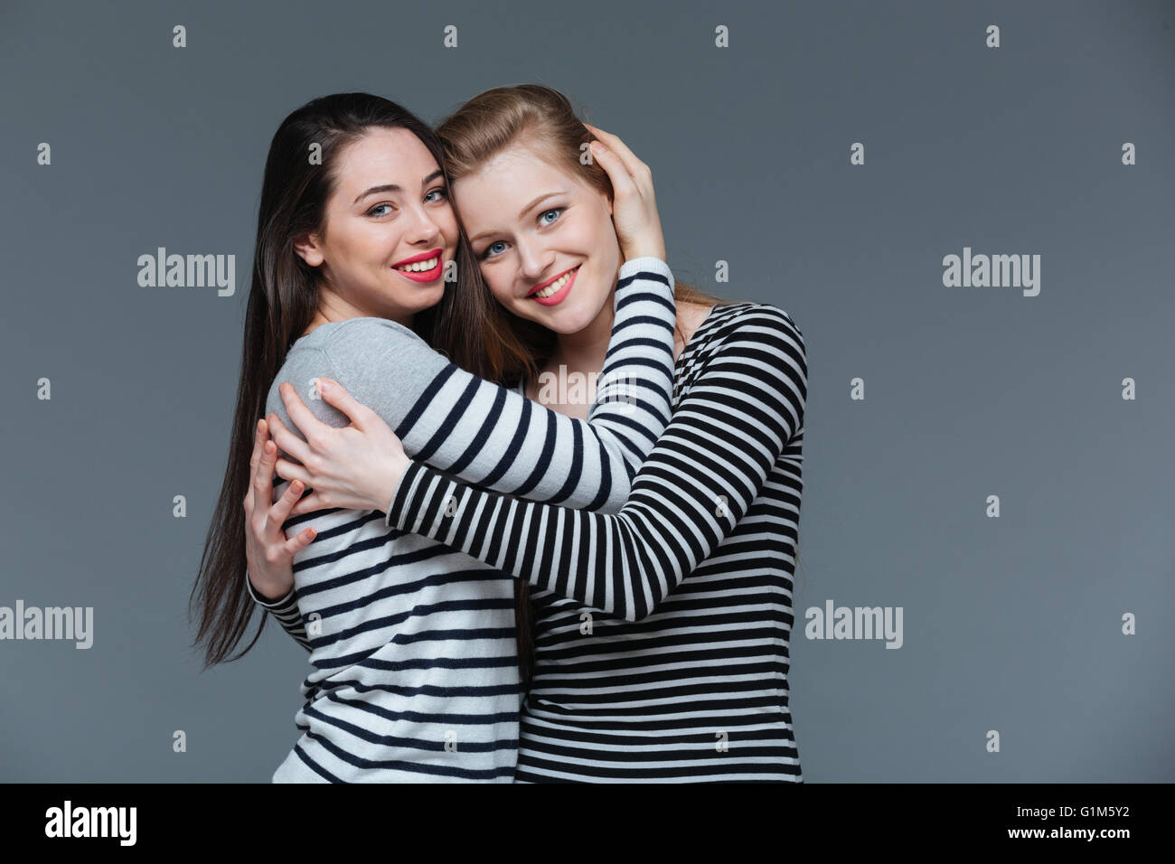 Portrait of two smiling attractive young women standing and hugging ...